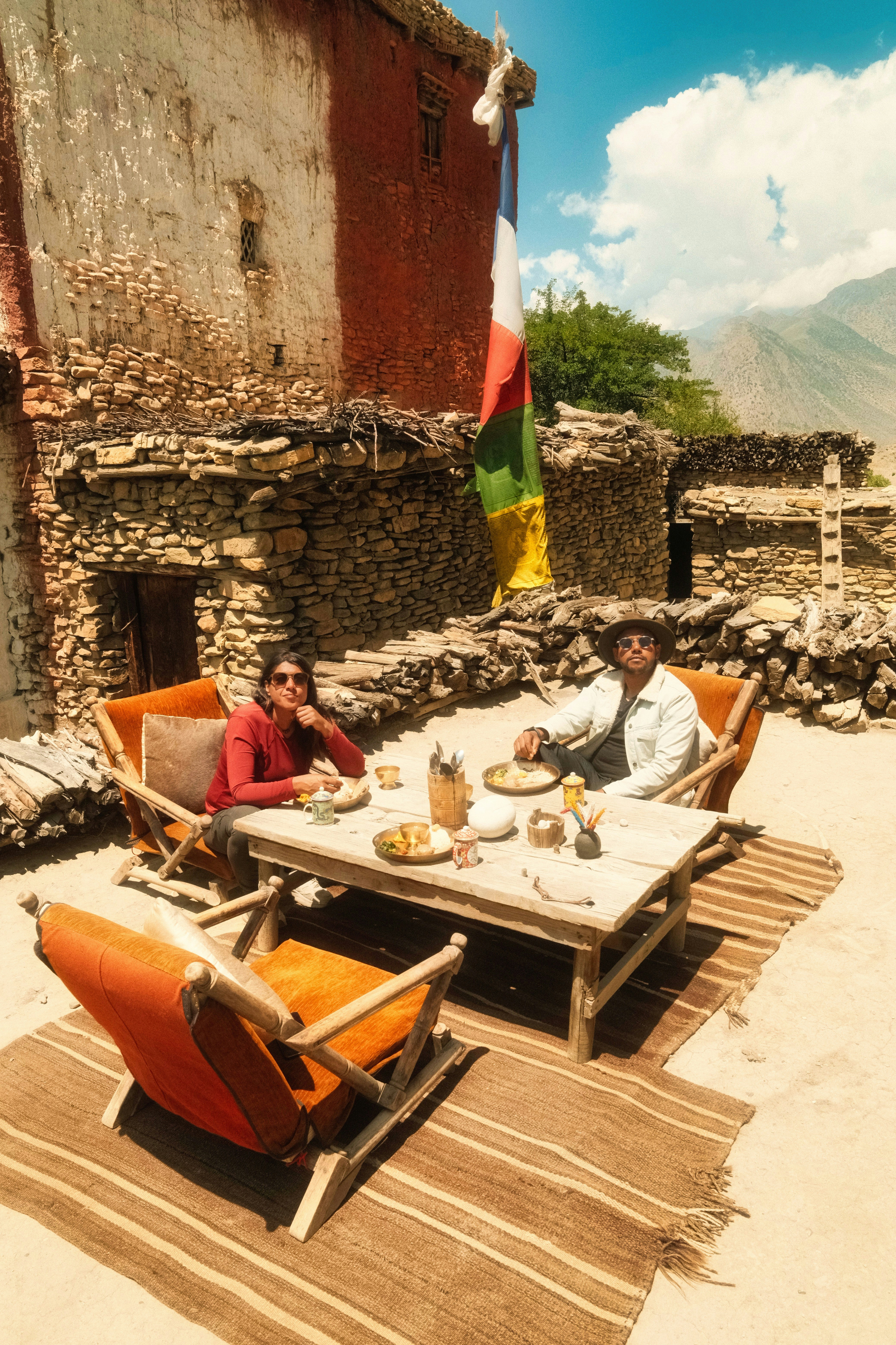Outdoor hillside cafe: a duo enjoys a sunlit meal amid rustic stone walls