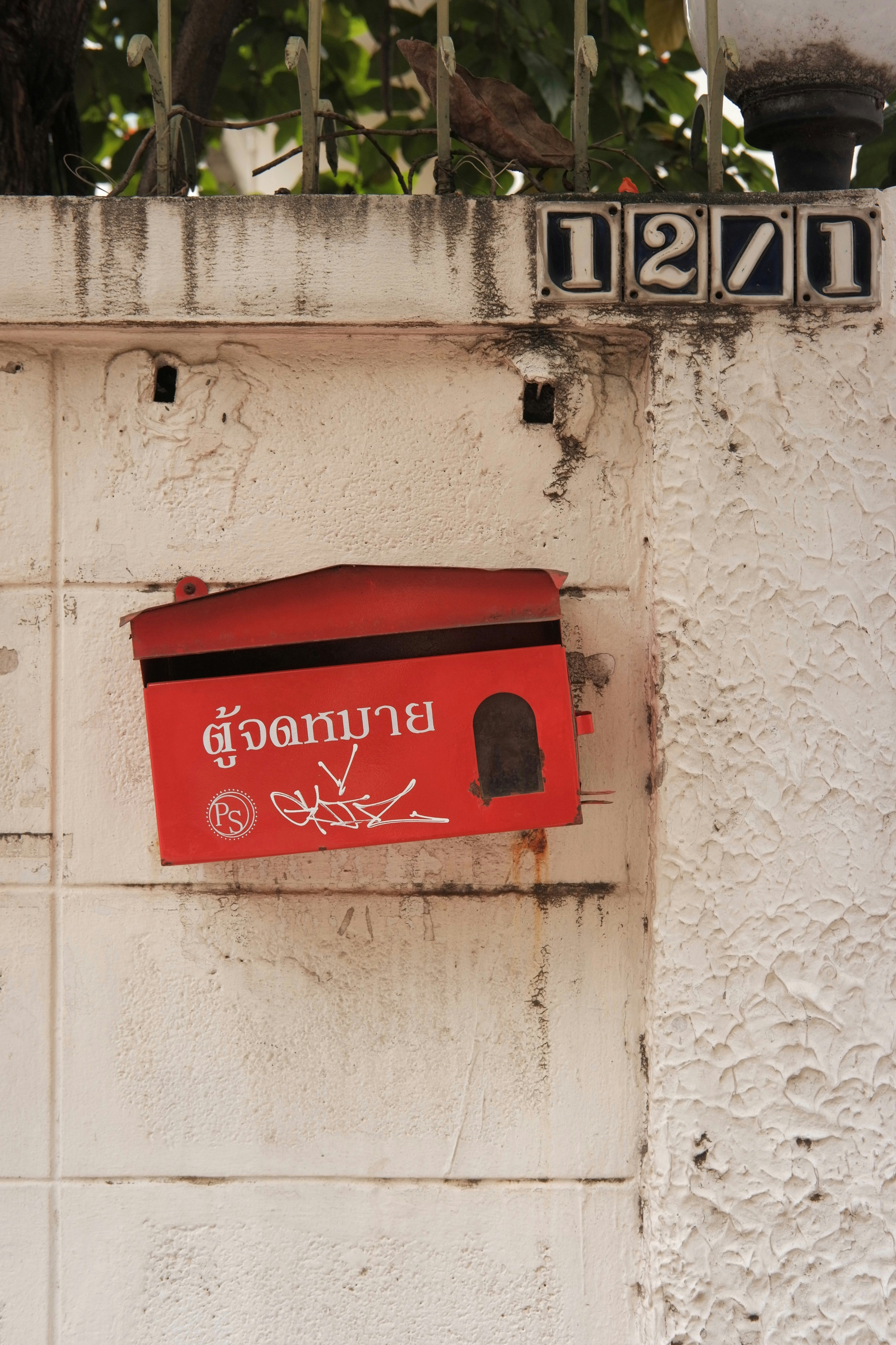 Red Mailbox on Weathered Wall Beneath Black Metal Rail