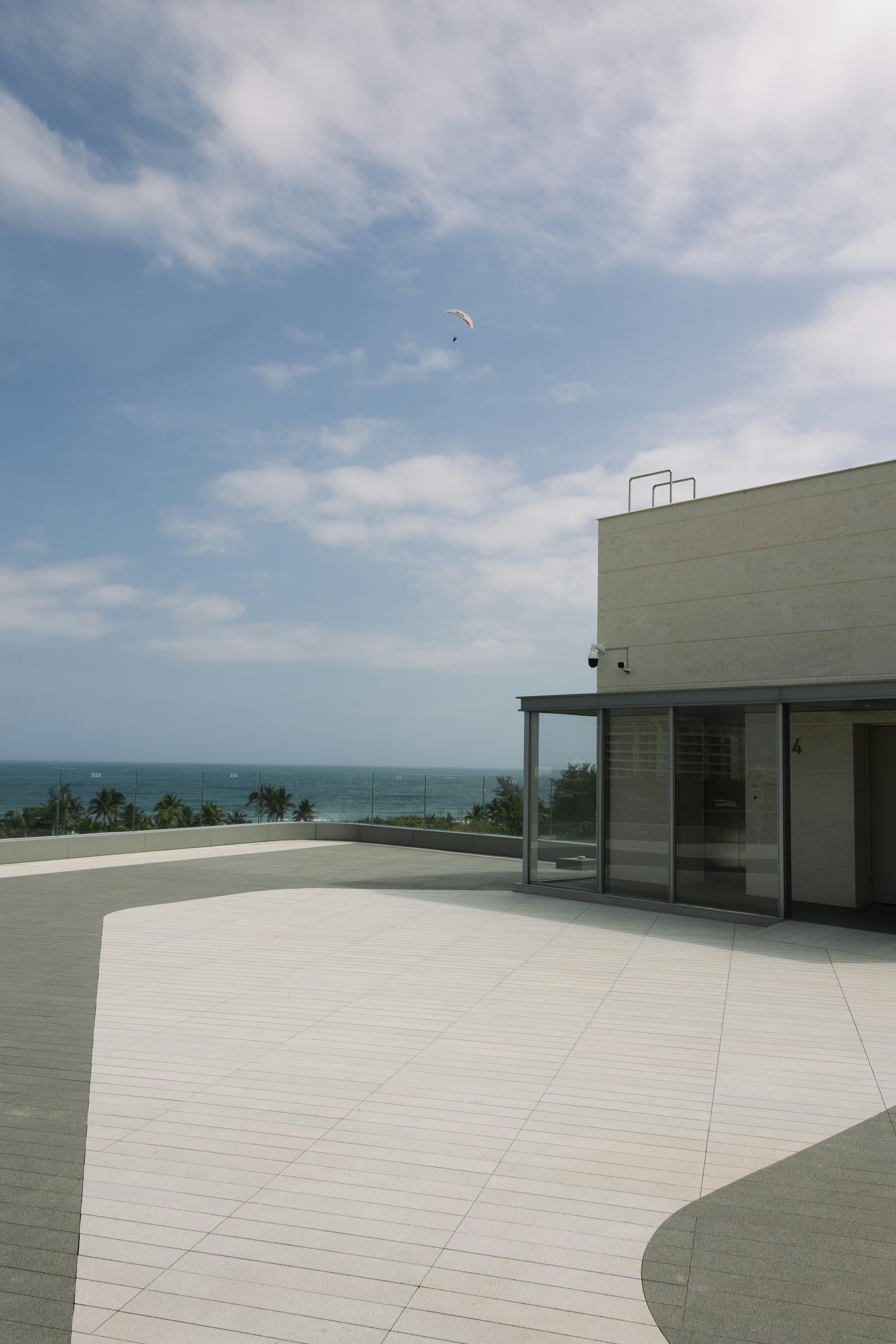 Rooftop Terrace Over Ocean: Quiet Geometry and Distant Parachute