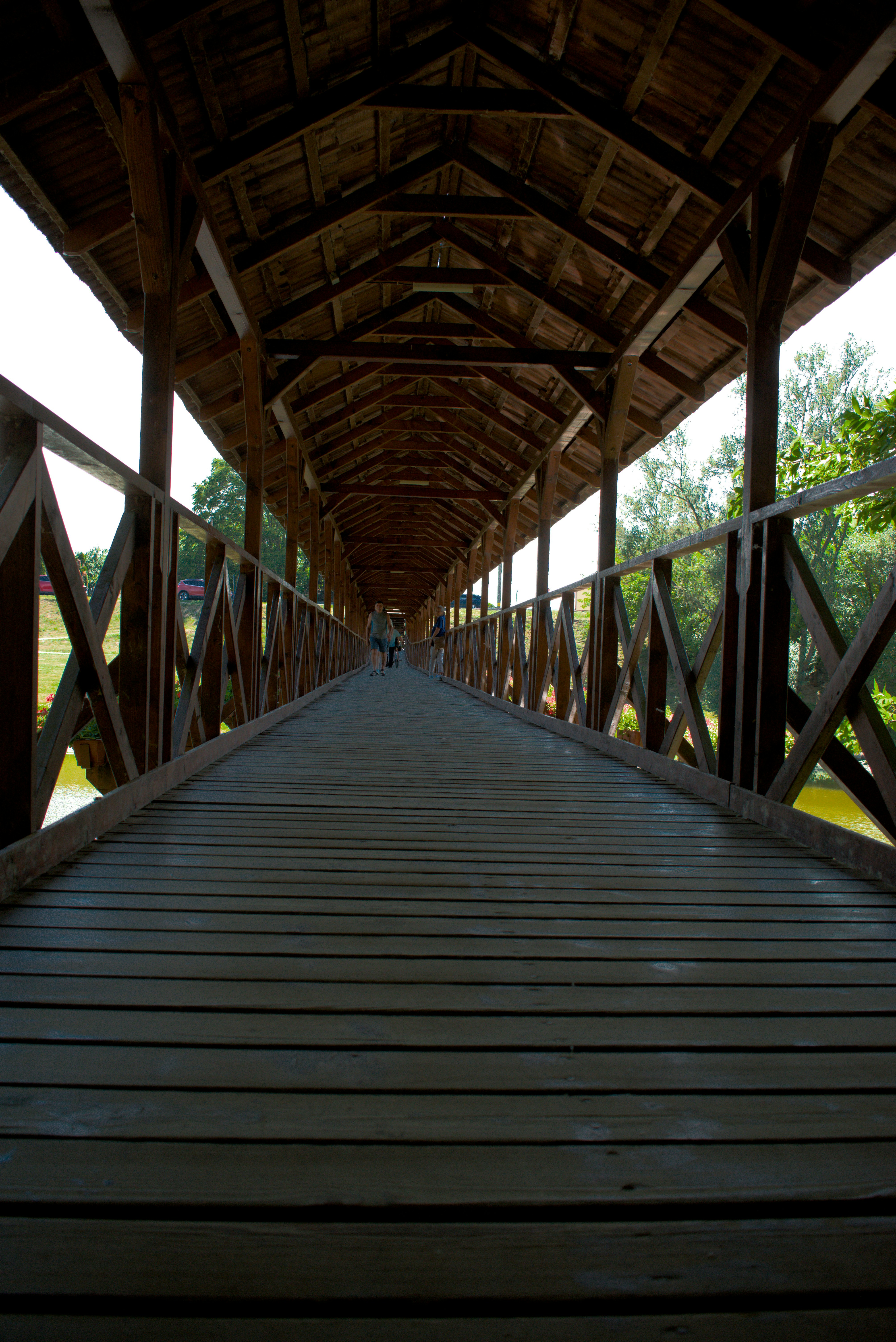 Pedestrian in the Center Aiming Down a Wooden Covered Bridge