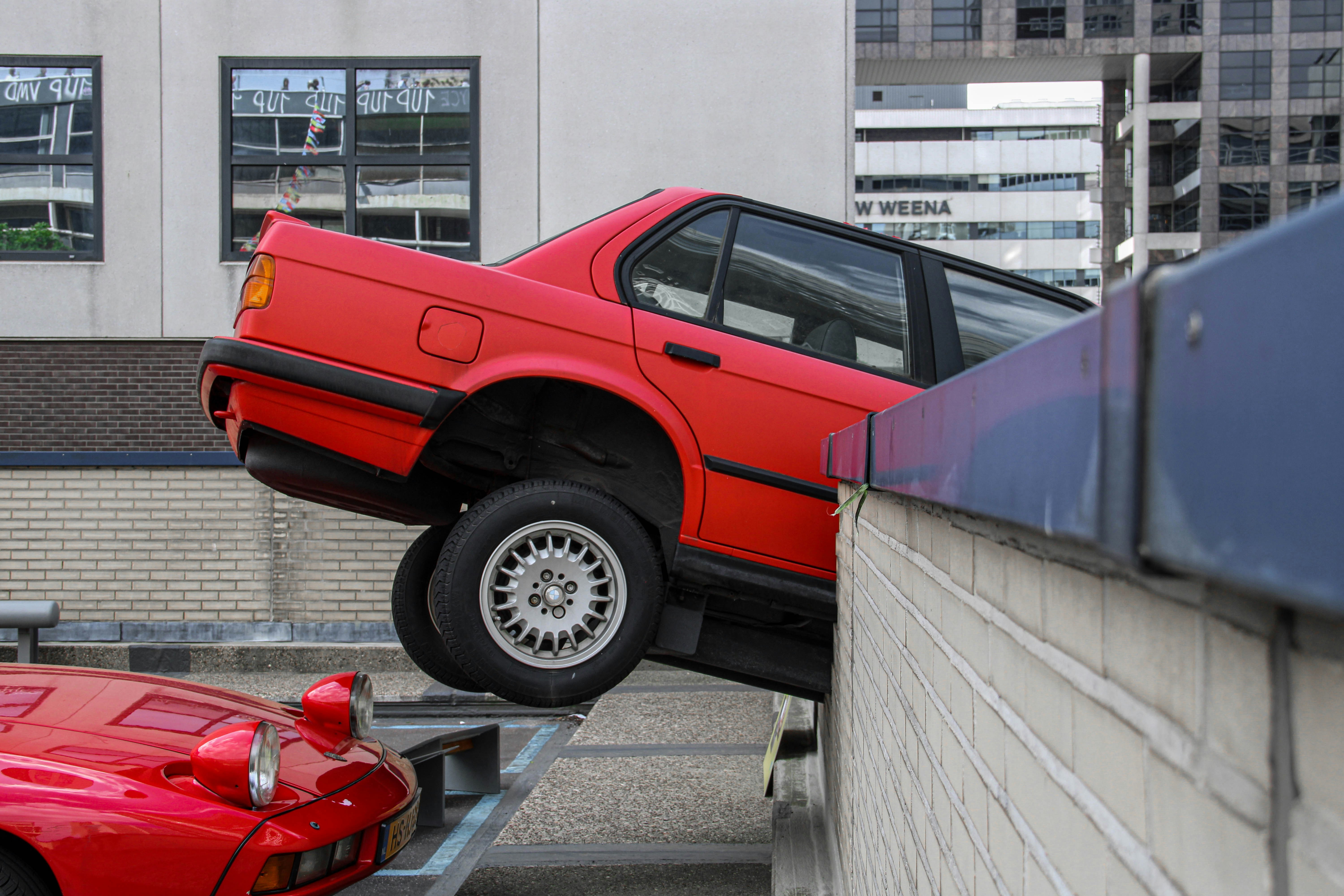 Tilted Red Coupe: A Car Teetering on the Edge of a Parking Wall