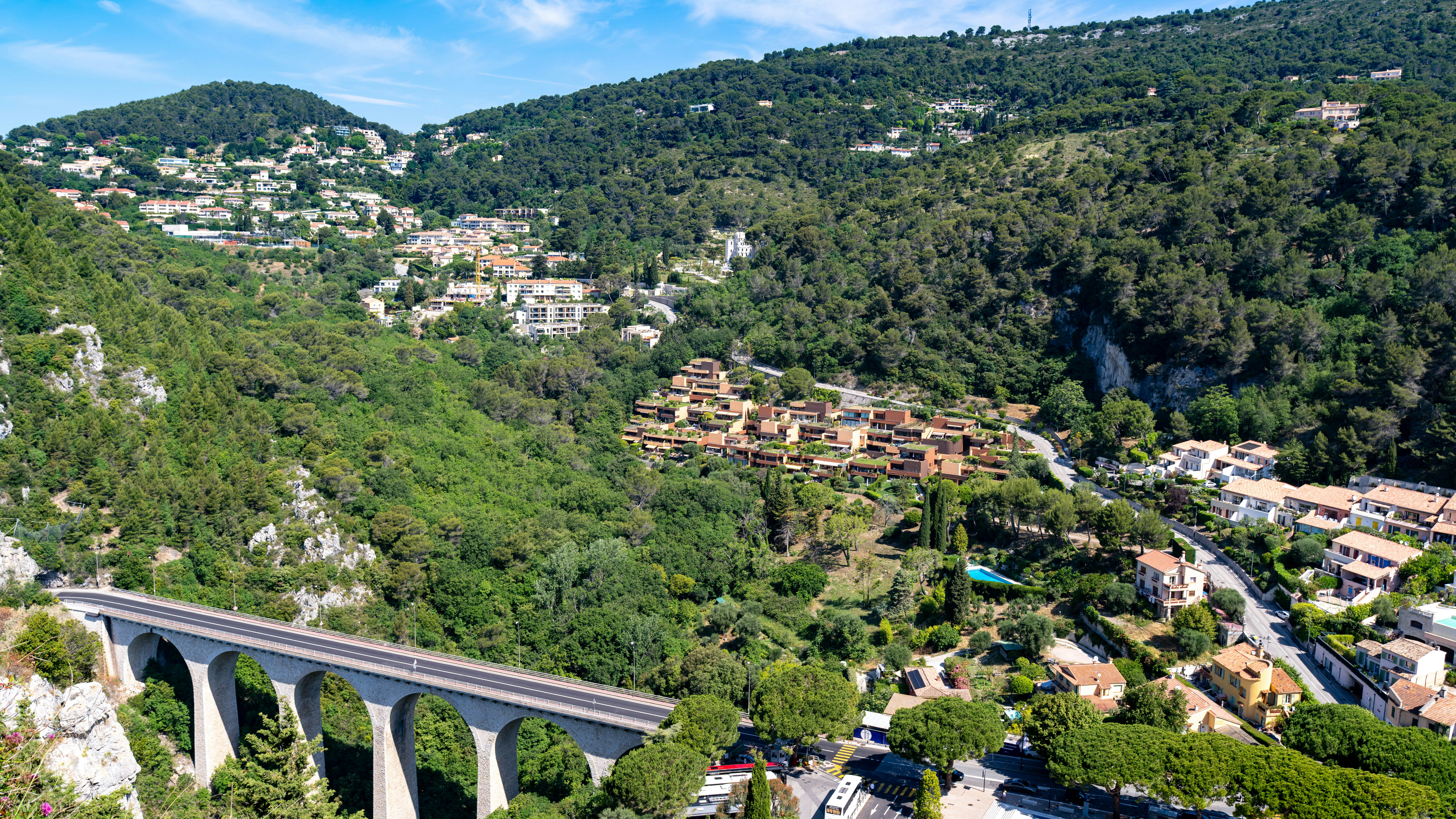 Terraced village tucked along a sunlit hillside, with an arched viaduct cutting through