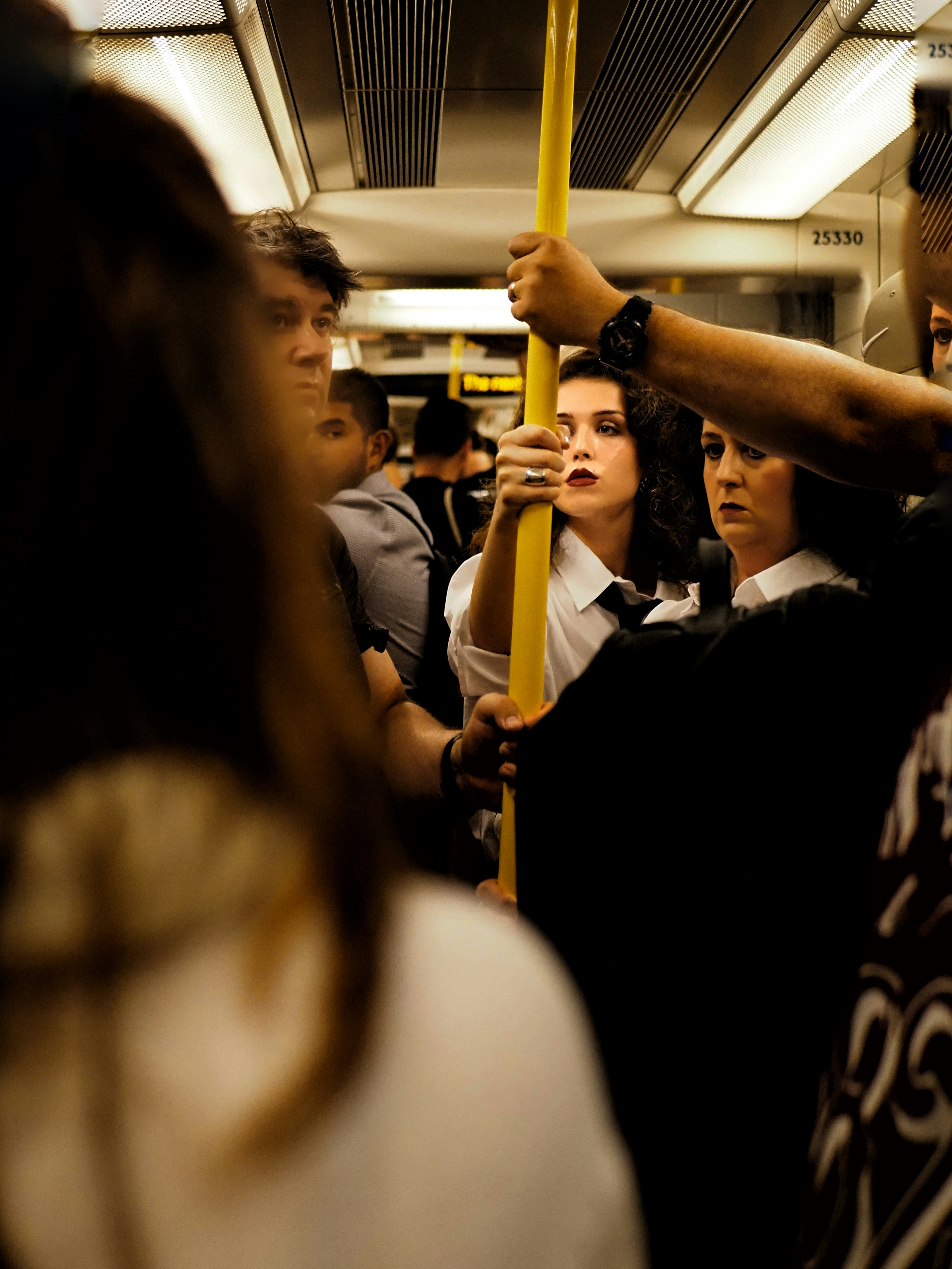 Mid-commute Intensity: A Woman Reaches for the Pole Amid a Sea of Faces