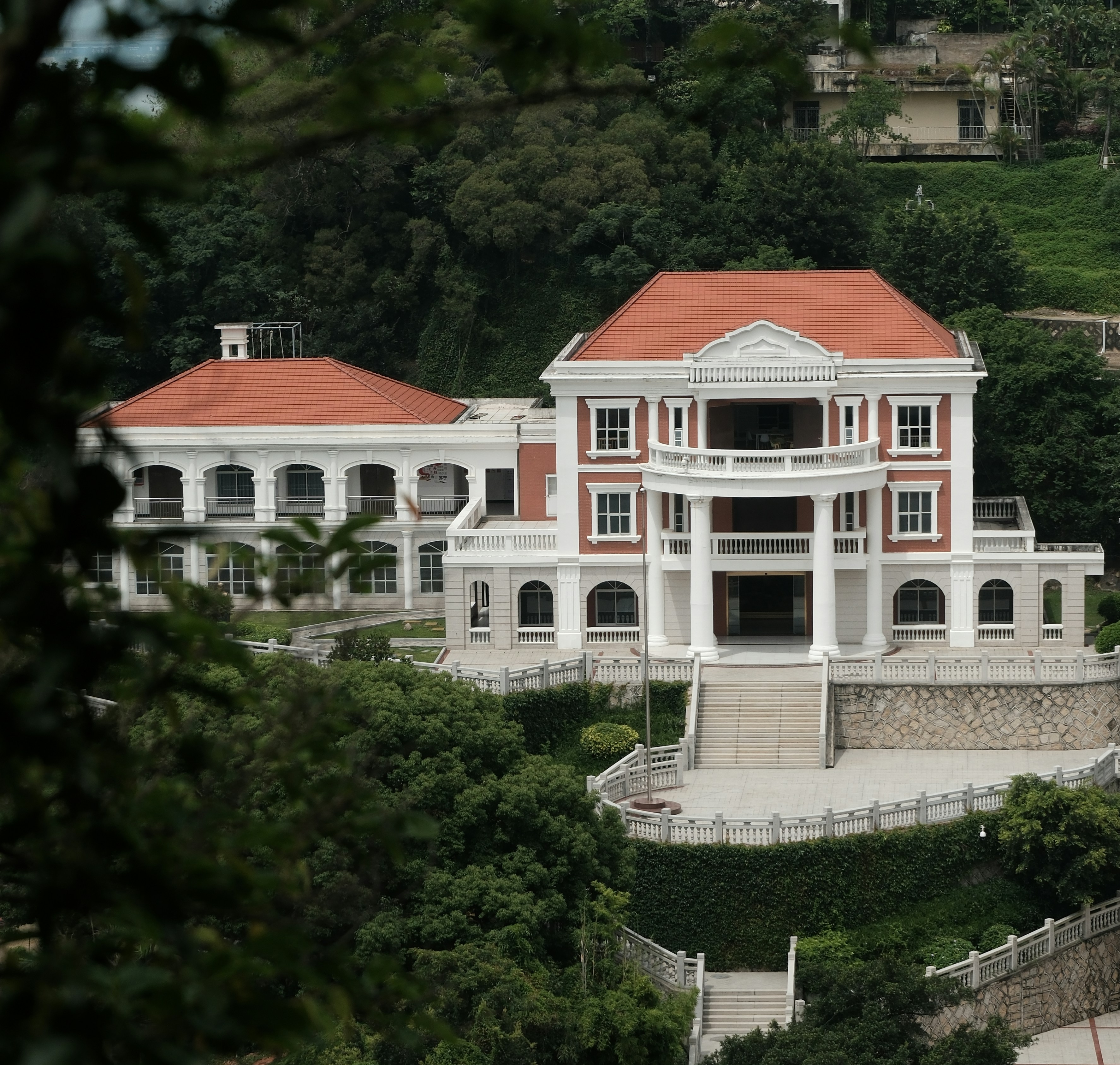 Grand Villa on a hillside: white neoclassical facade with red-tiled roof framed by greenery
