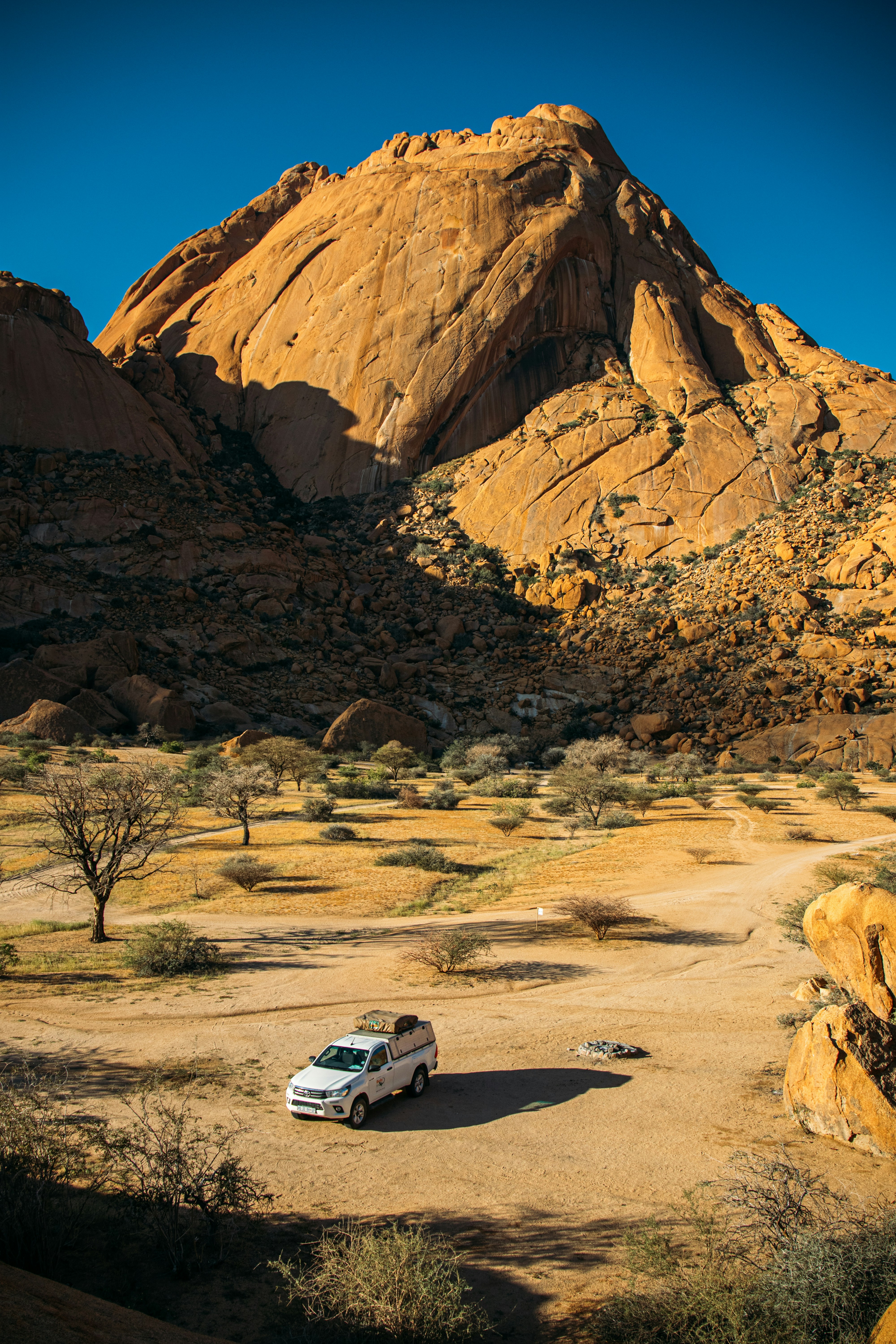Desert Monolith: A White Vehicle at the Foot of a Golden Cliff