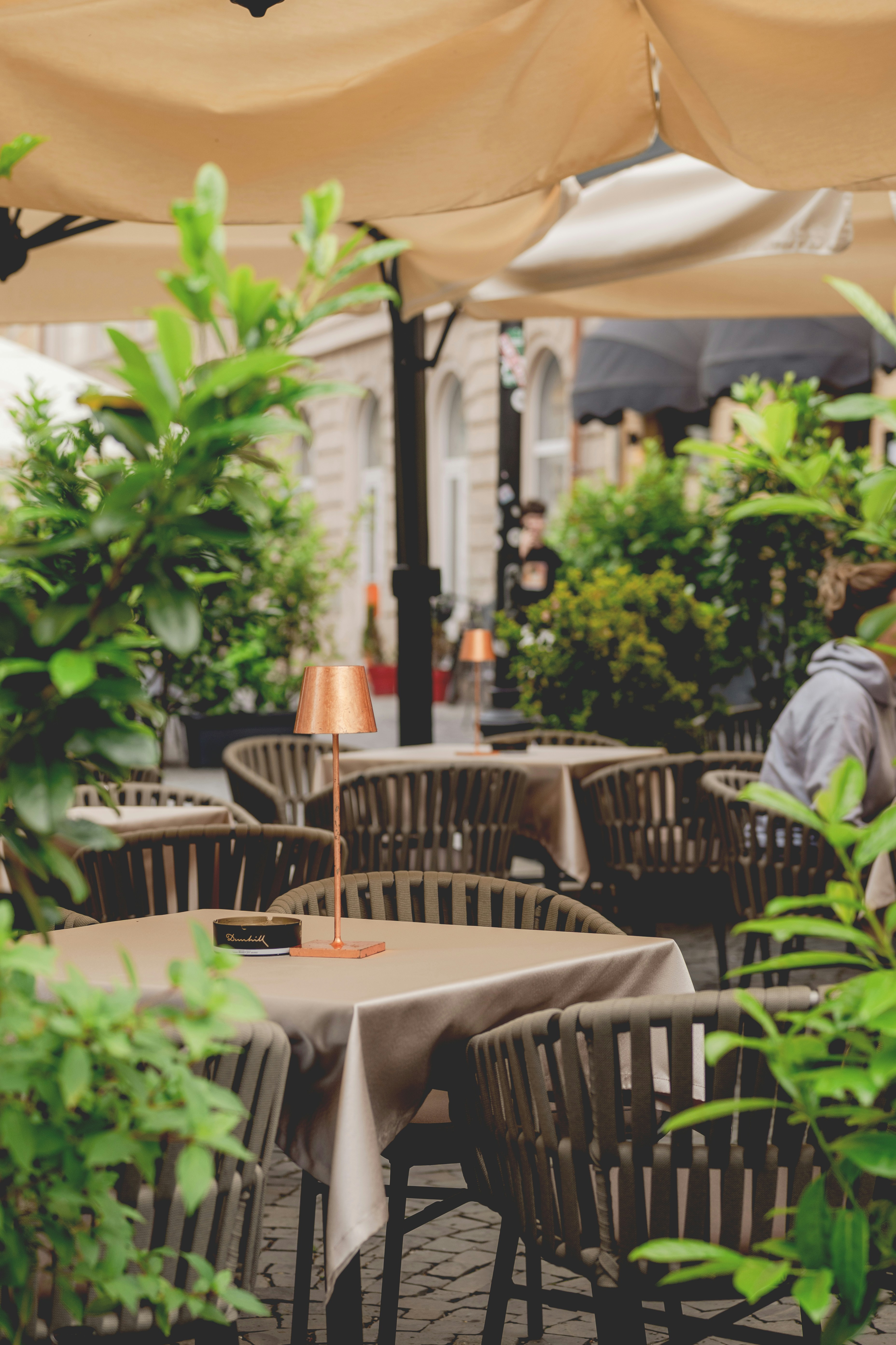 Garden cafe hush: copper lamp on a softly set table amid lush greenery