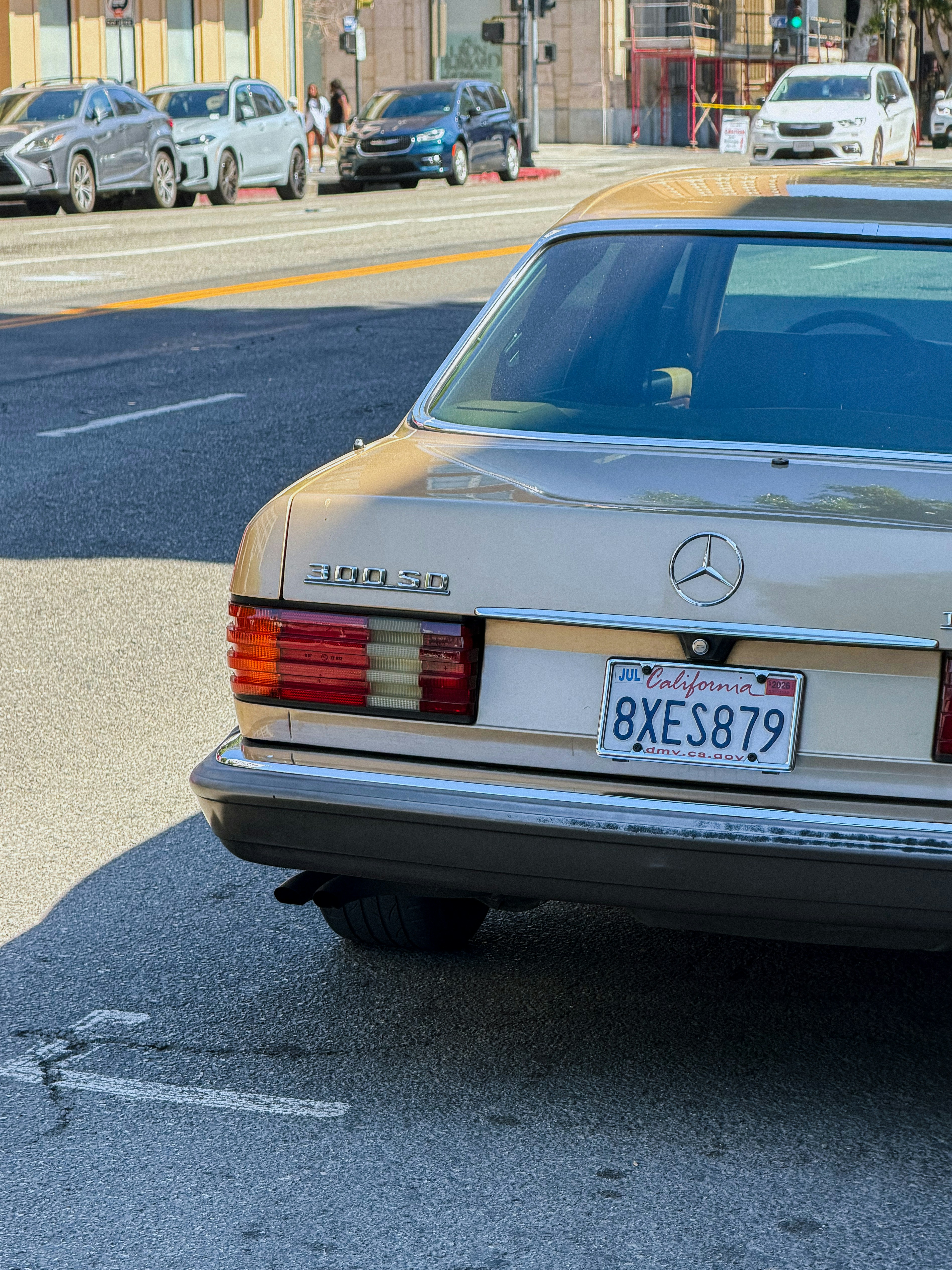 European sedan on a sunlit street, rear view framing a parked Mercedes and license plate