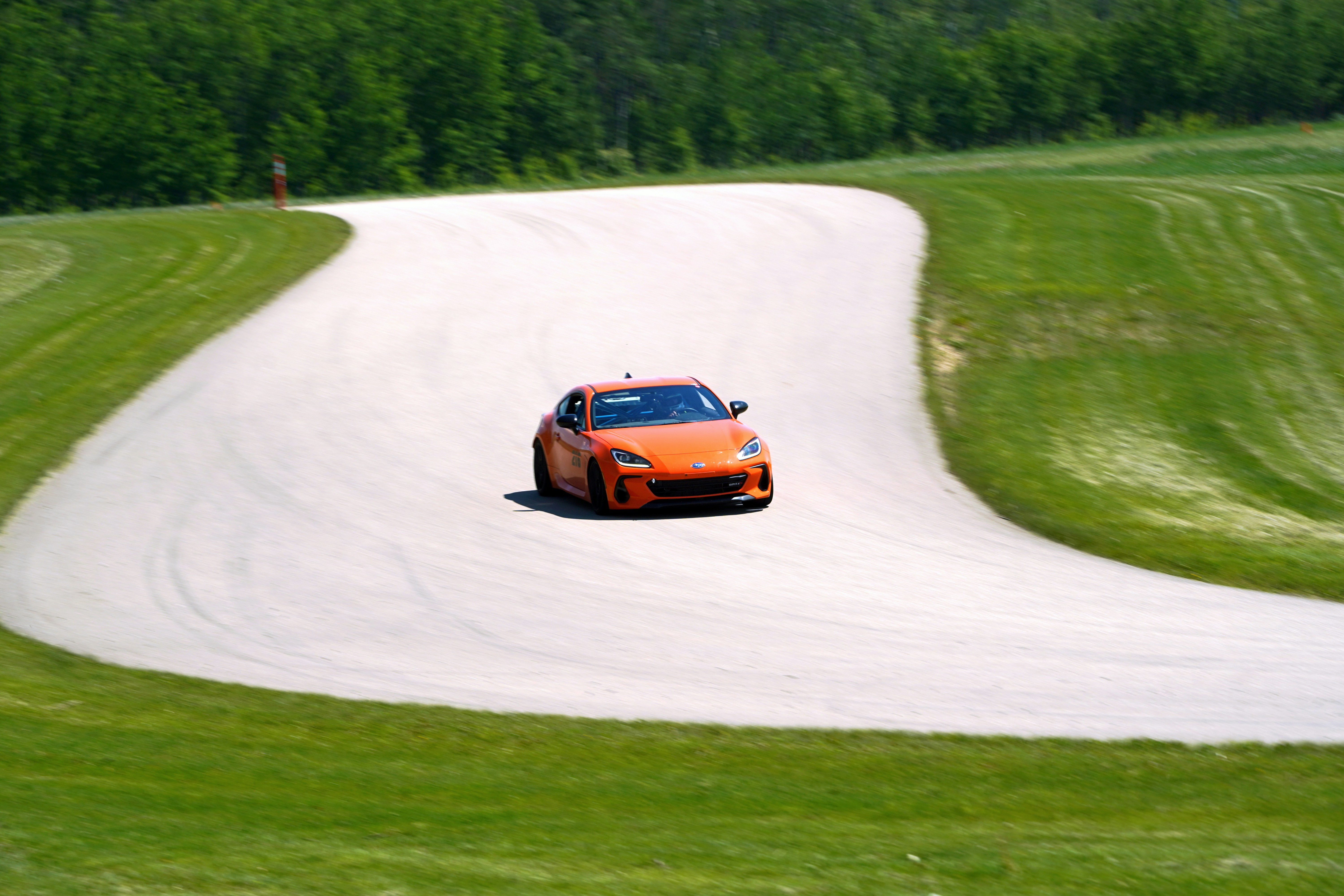 Bright orange sports car navigating a curved road amid green fields; a dynamic, panned capture emphasizing motion and speed.
