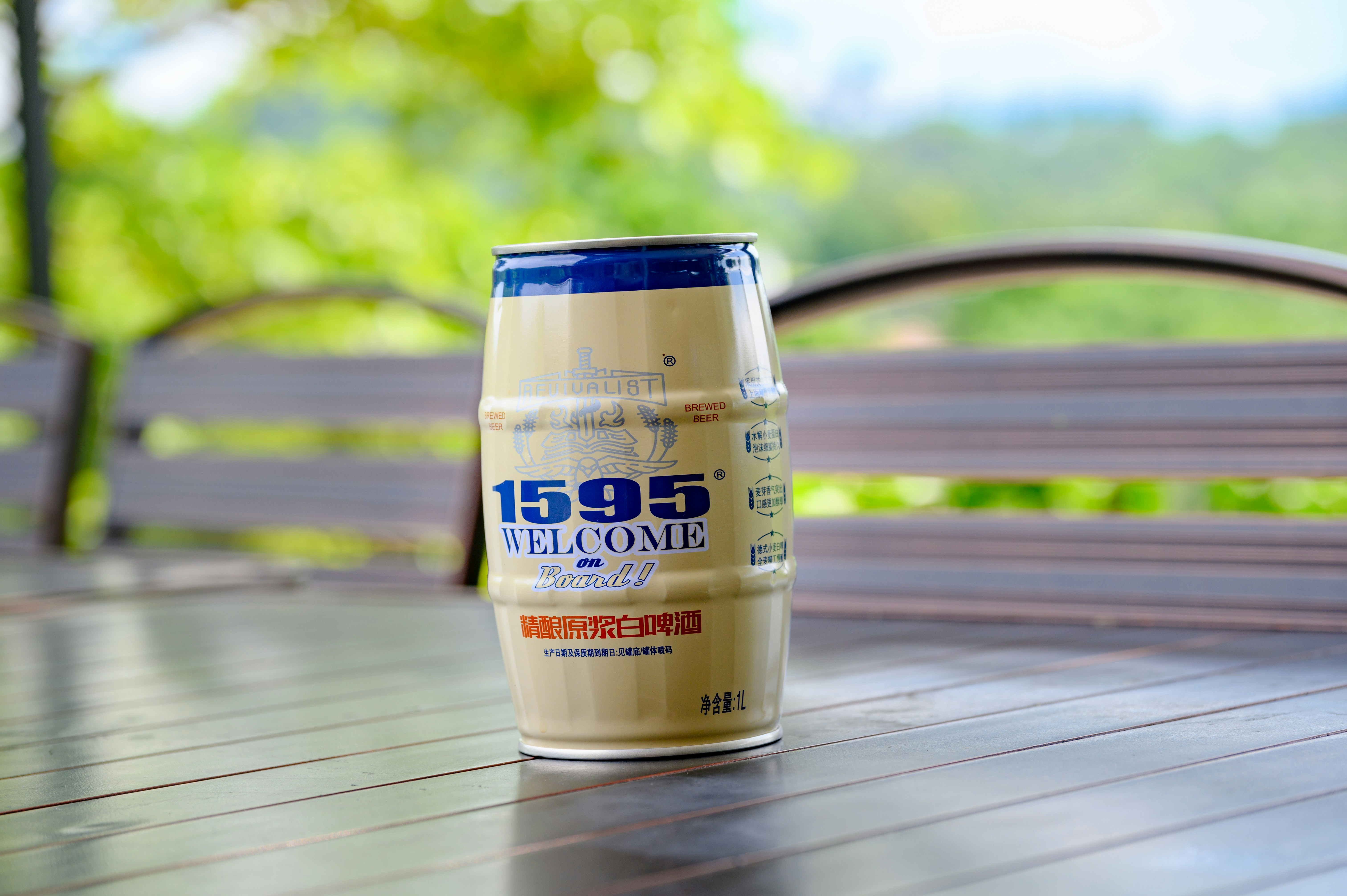 A single can rests on a wooden outdoor table with a blurred green background, emphasizing product detail and label.