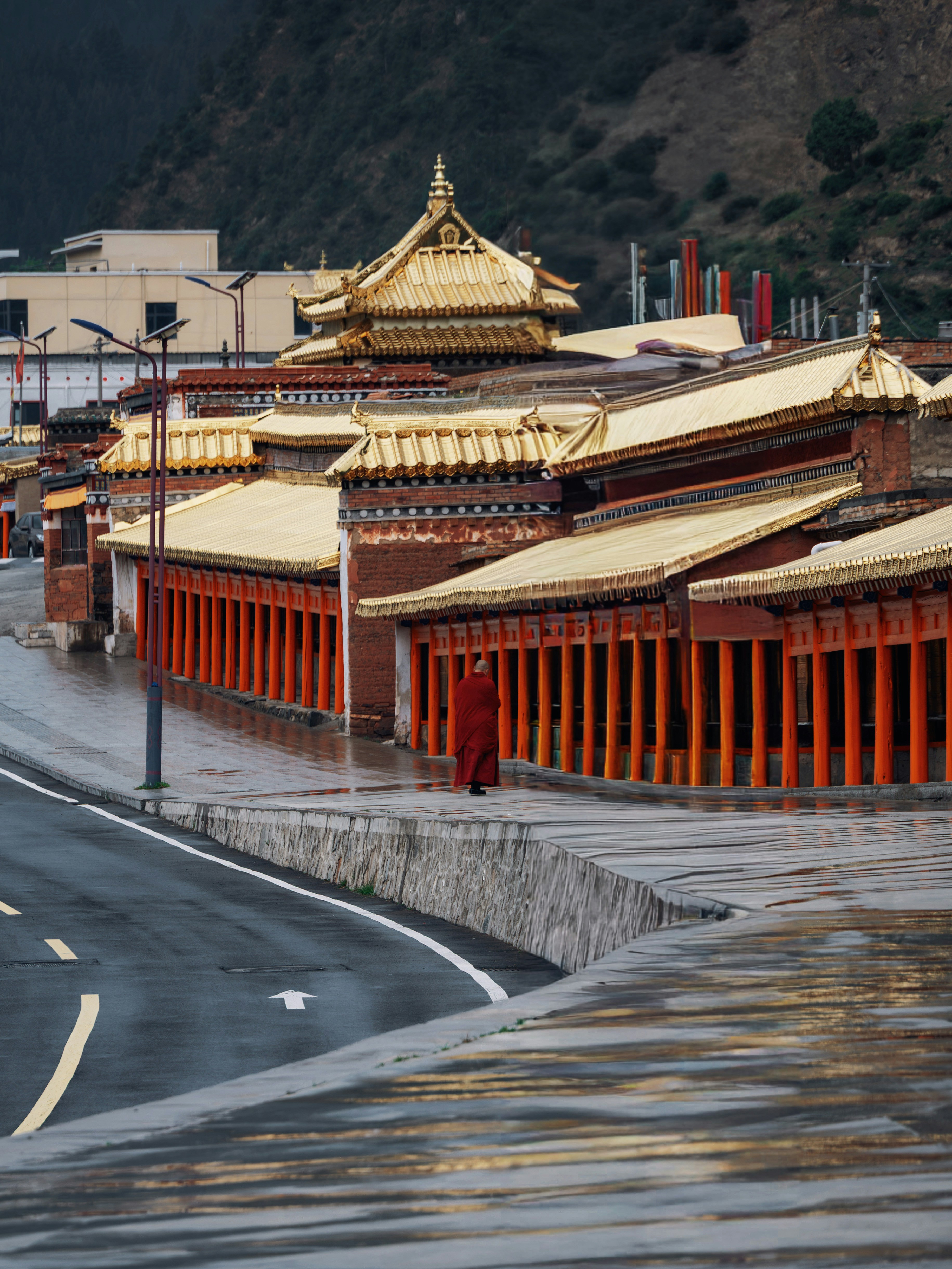 A monk walks past a golden-roofed temple in mountains