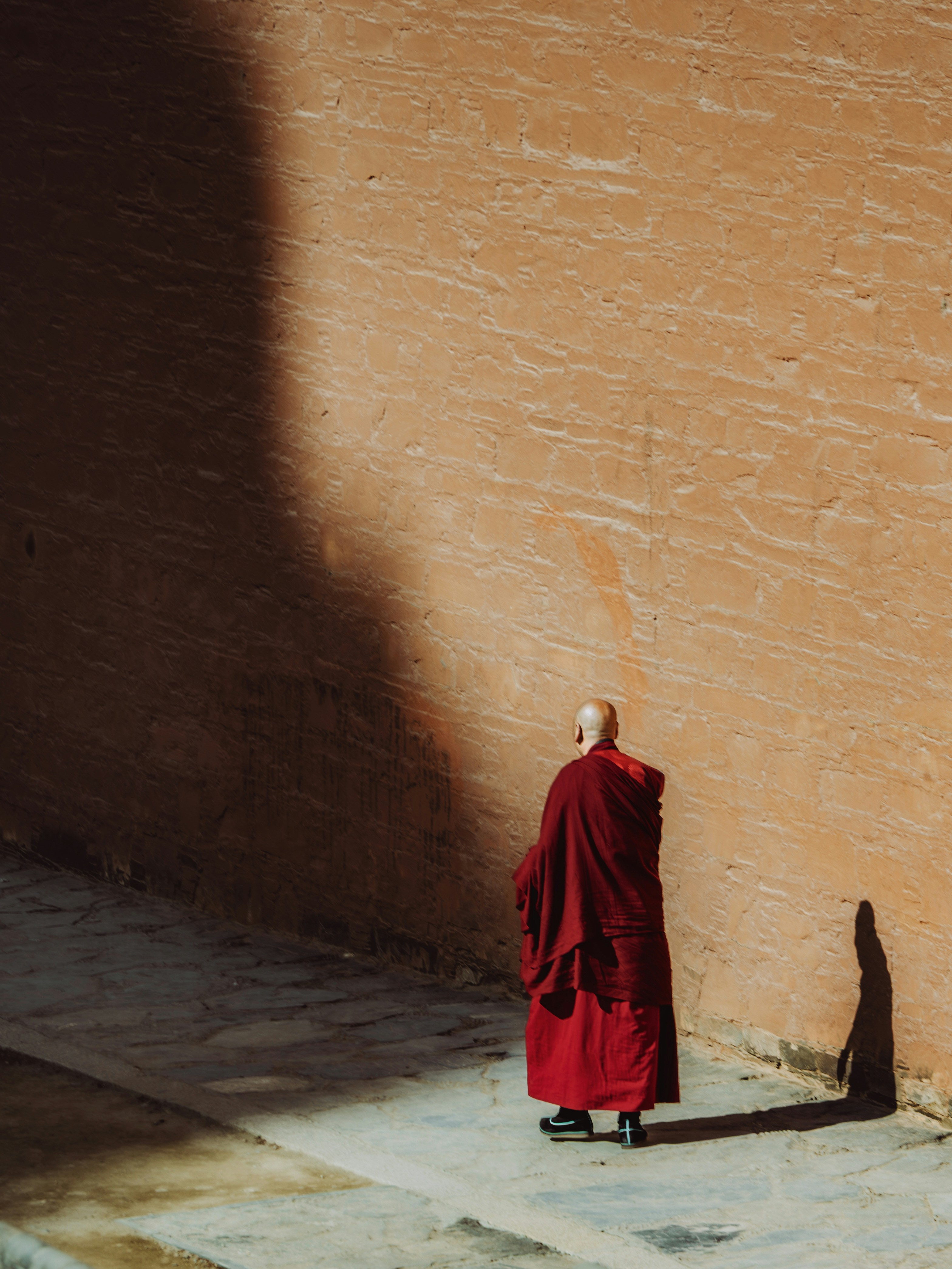 Red-robed wanderer casts a long shadow along sunlit stucco