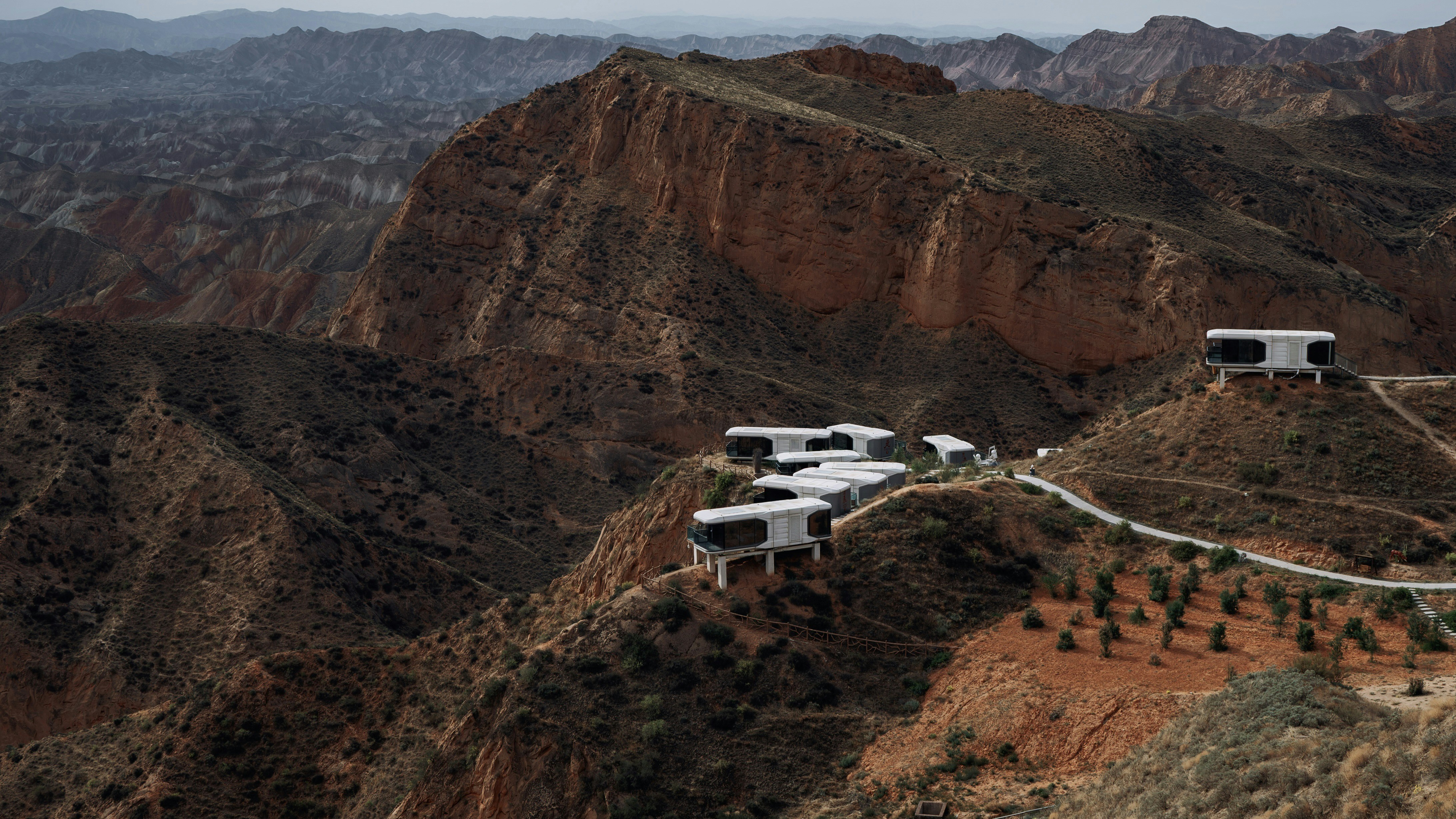 Cliffside Caravan: A Serene White-Walled Road of Vehicles Among Desert Gorges