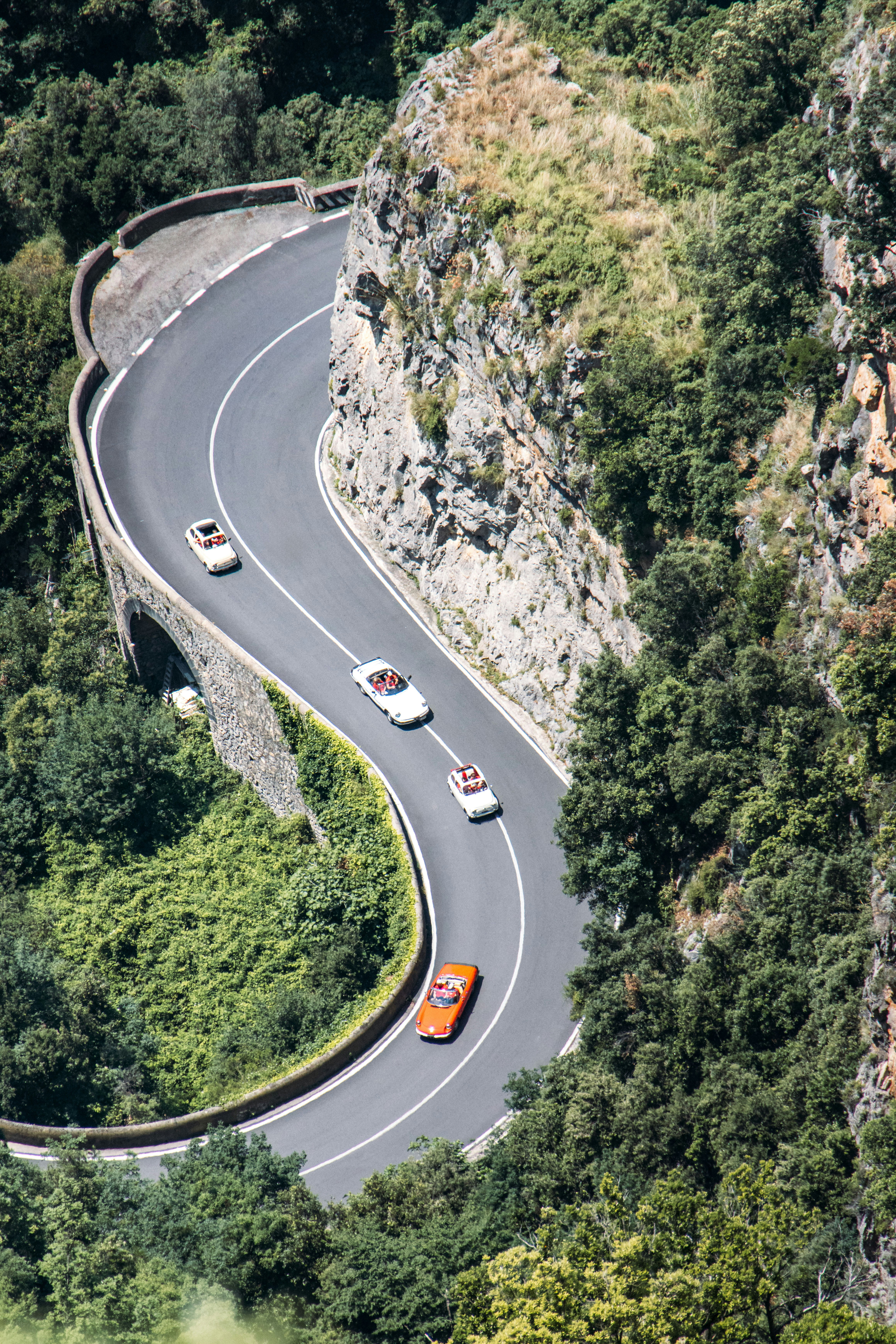 Serpentine Ascent: A Line of Classic Convertibles Winding Through a Mountain Pass