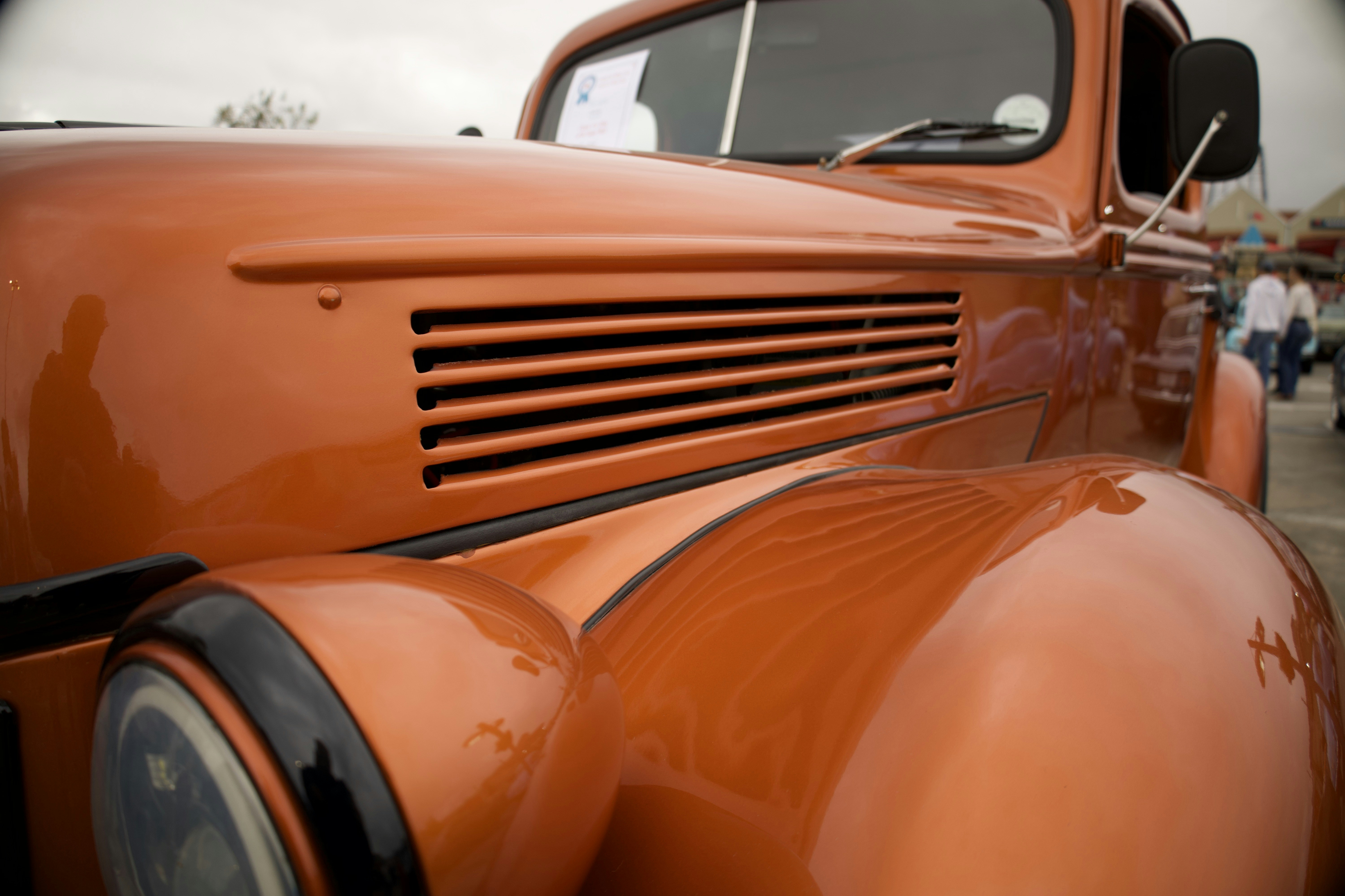 Glossy orange vintage car's hood, fender, and grille.
