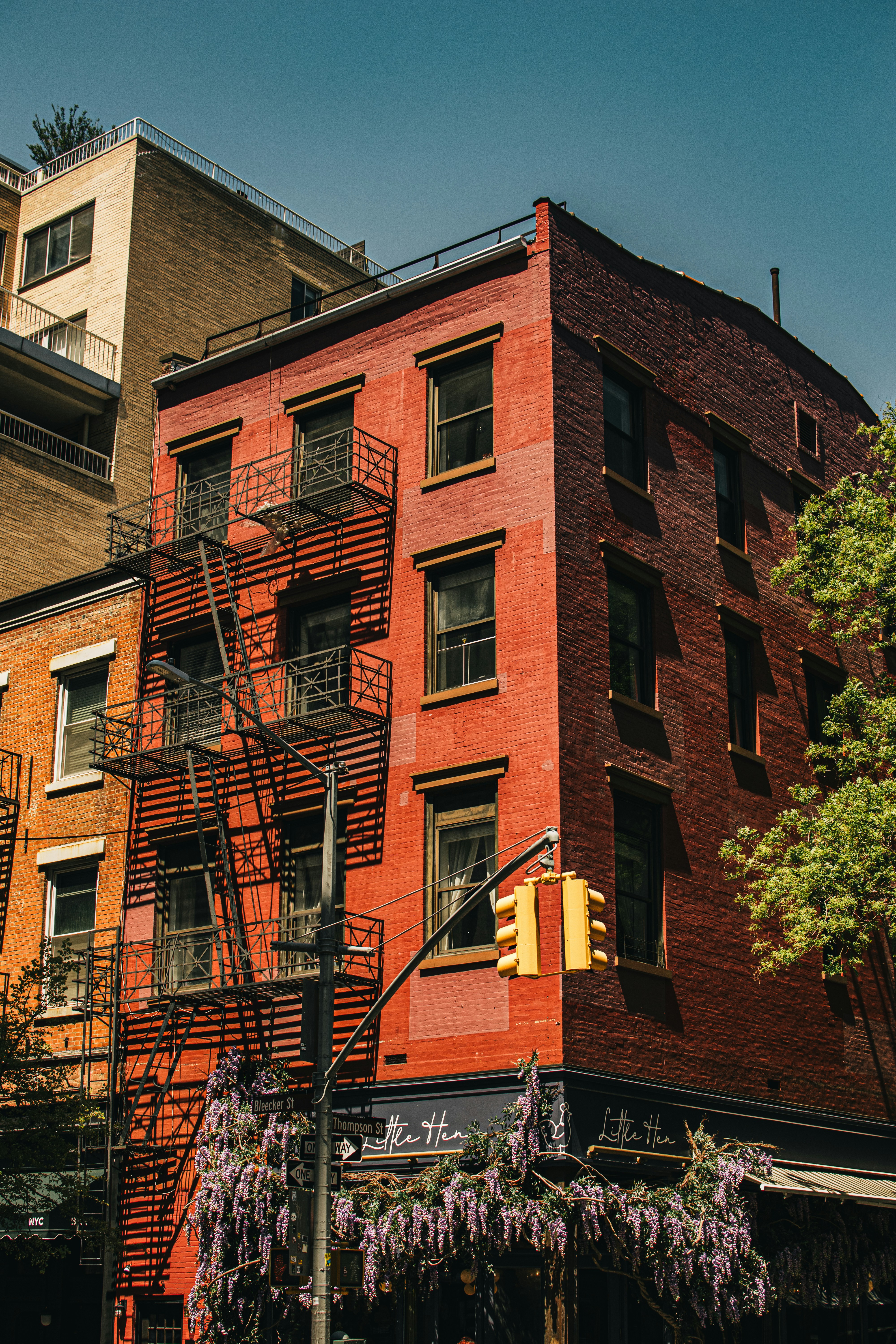 Red Brick Corner: Fire Escapes and Florals Framing a Sunlit Street
