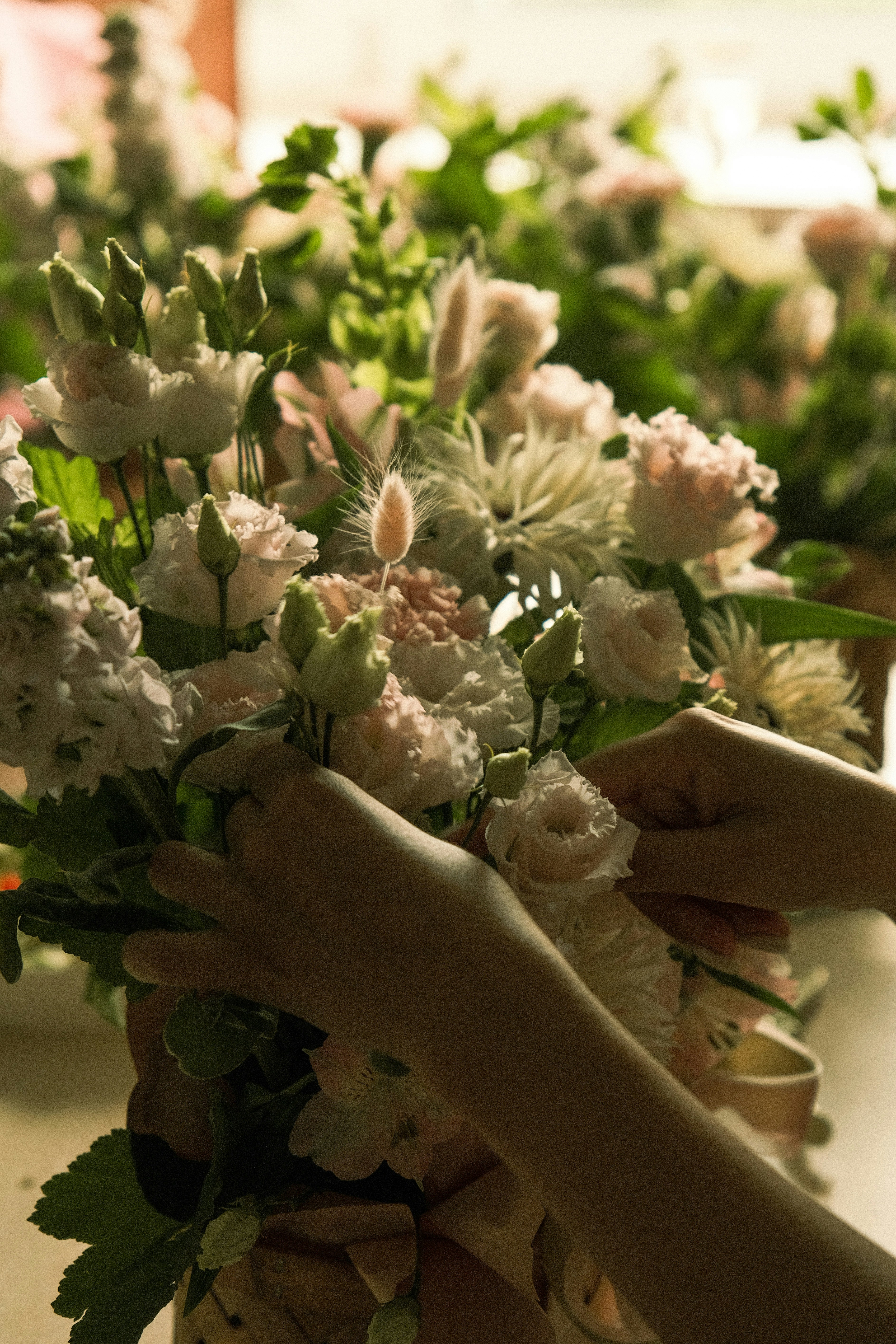 Hands attend to a blush bouquet in warm kitchen light