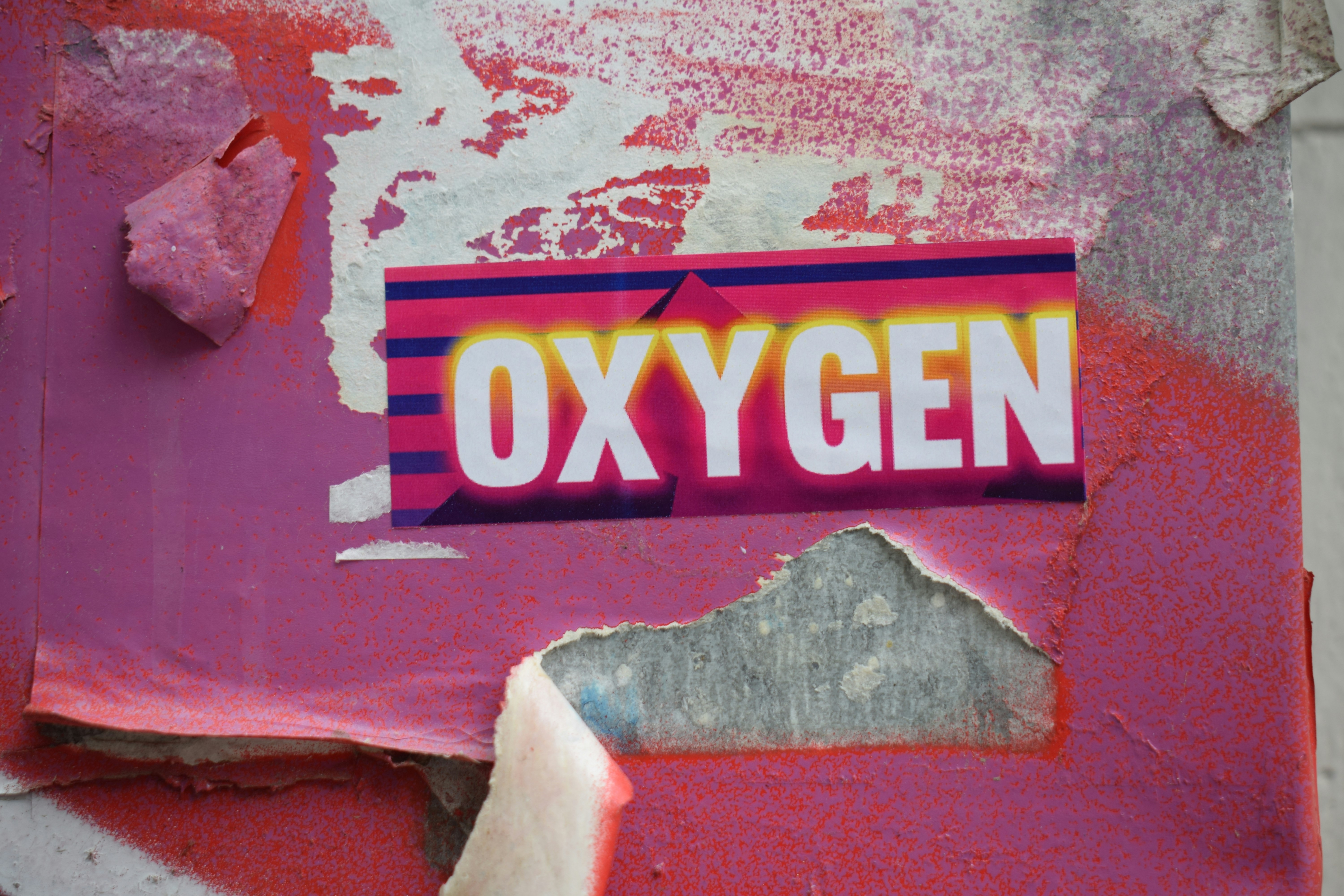 Sticker on a chipped pink wall: Oxygen in bold colors amidst peeling paint