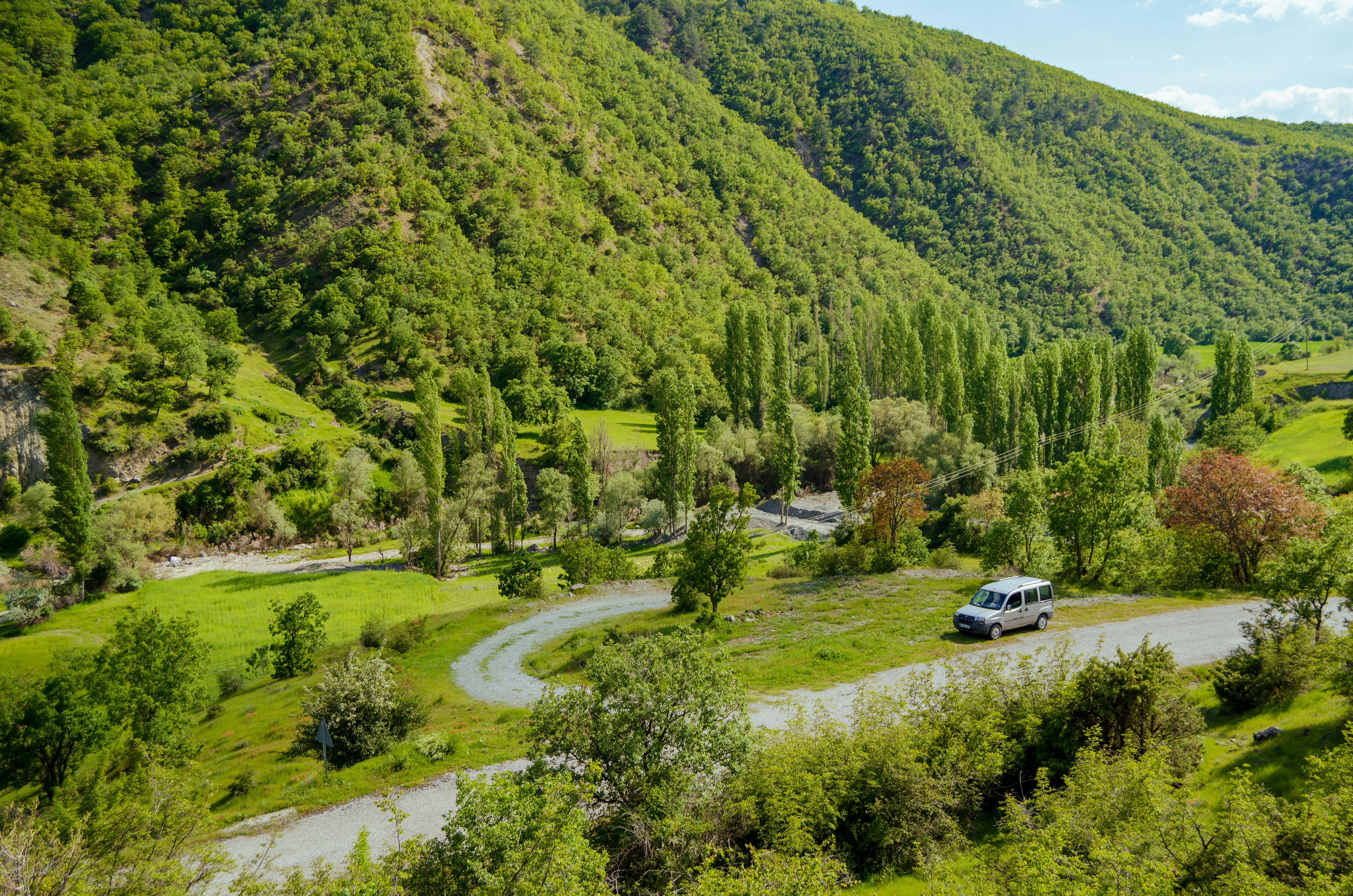 Winding Mountain Road: A Silver Car Navigates a Lush Valley