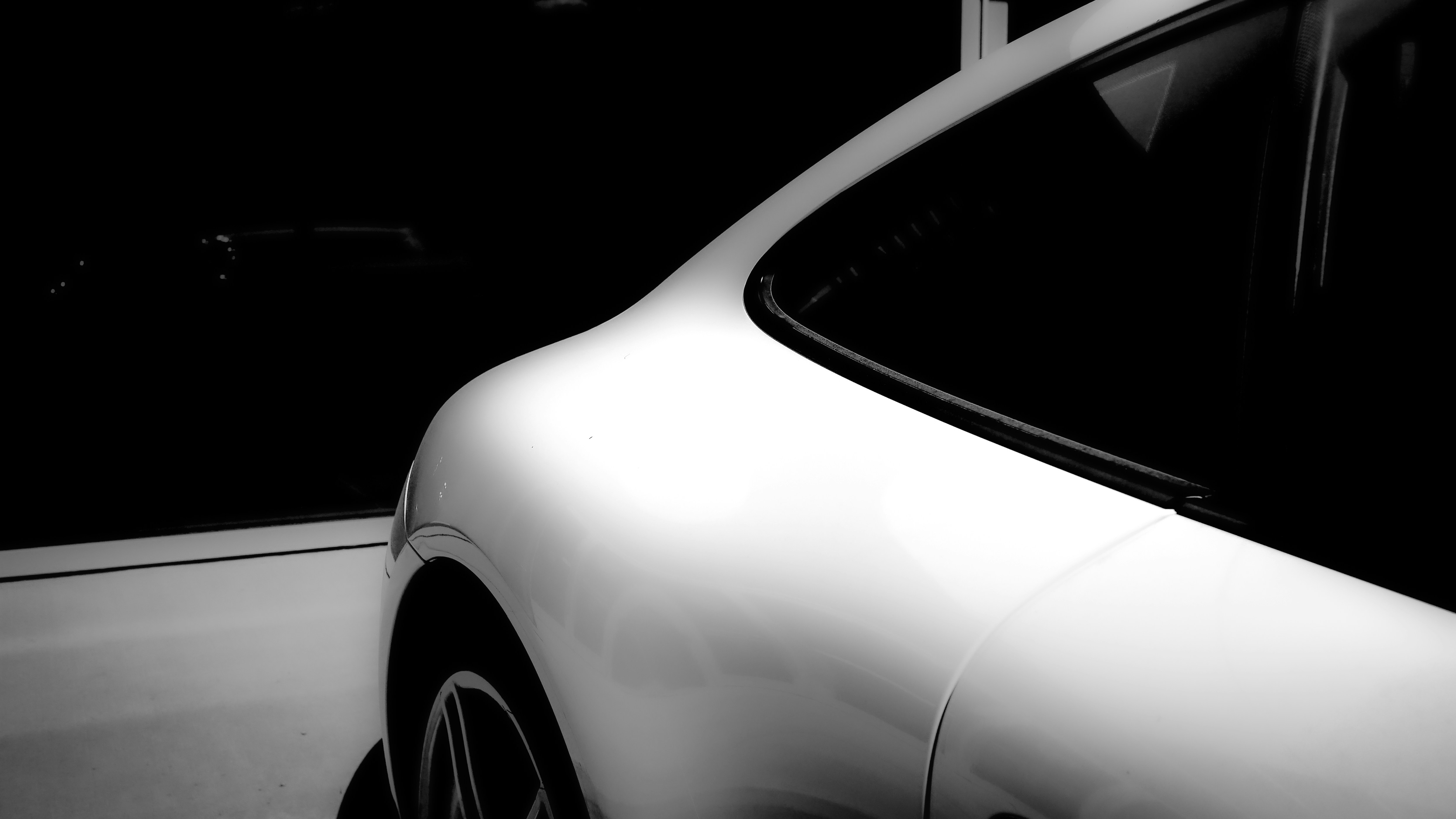 Sleek car body curving across a monochrome frame, emphasizing smooth surfaces and glossy finish; a close crop hints at automotive design details and form. Logo or branding not visible.