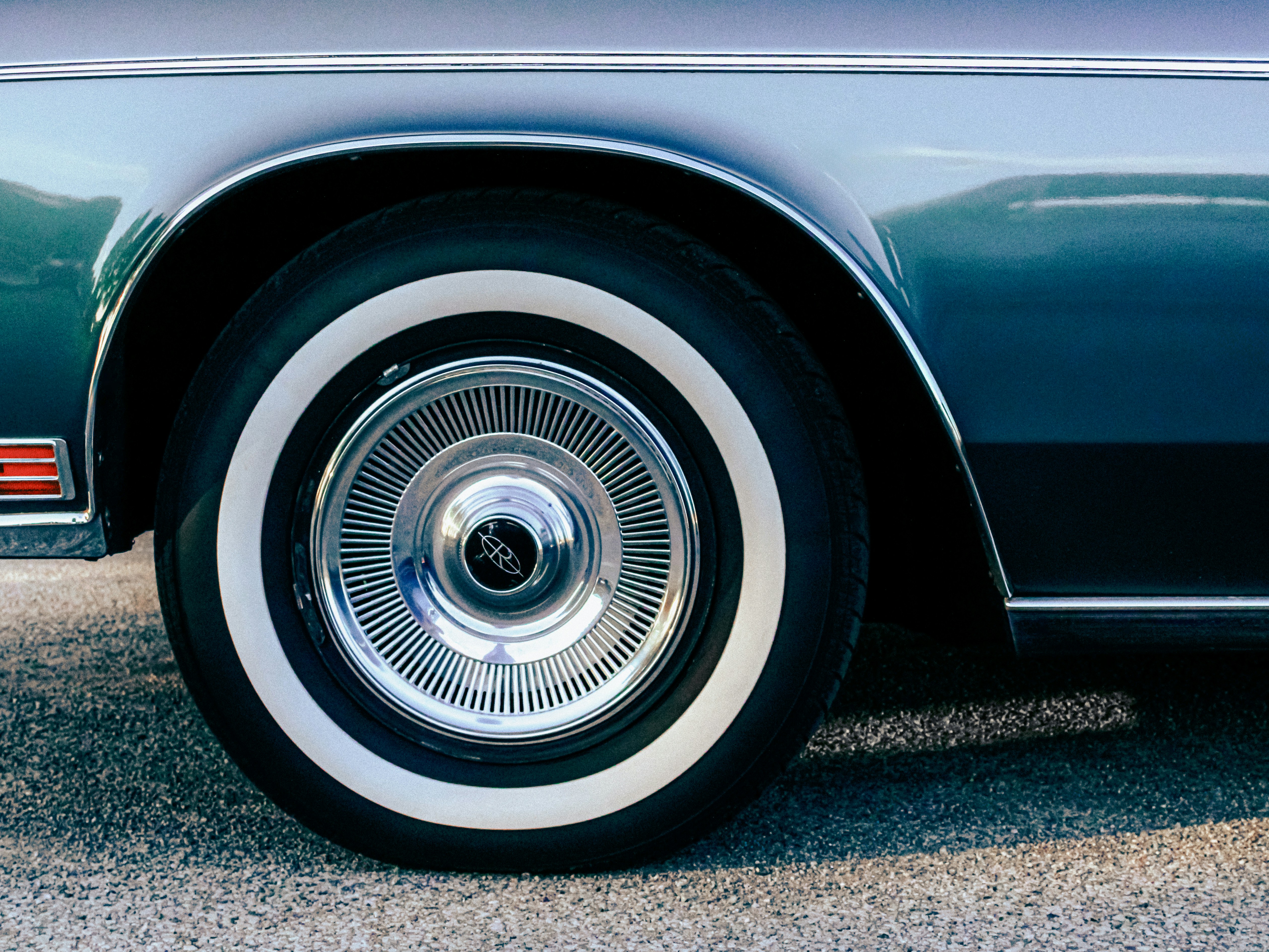Shiny vintage car wheel with chrome hubcap and whitewall tire sits in warm daylight, capturing a nostalgic automotive moment.