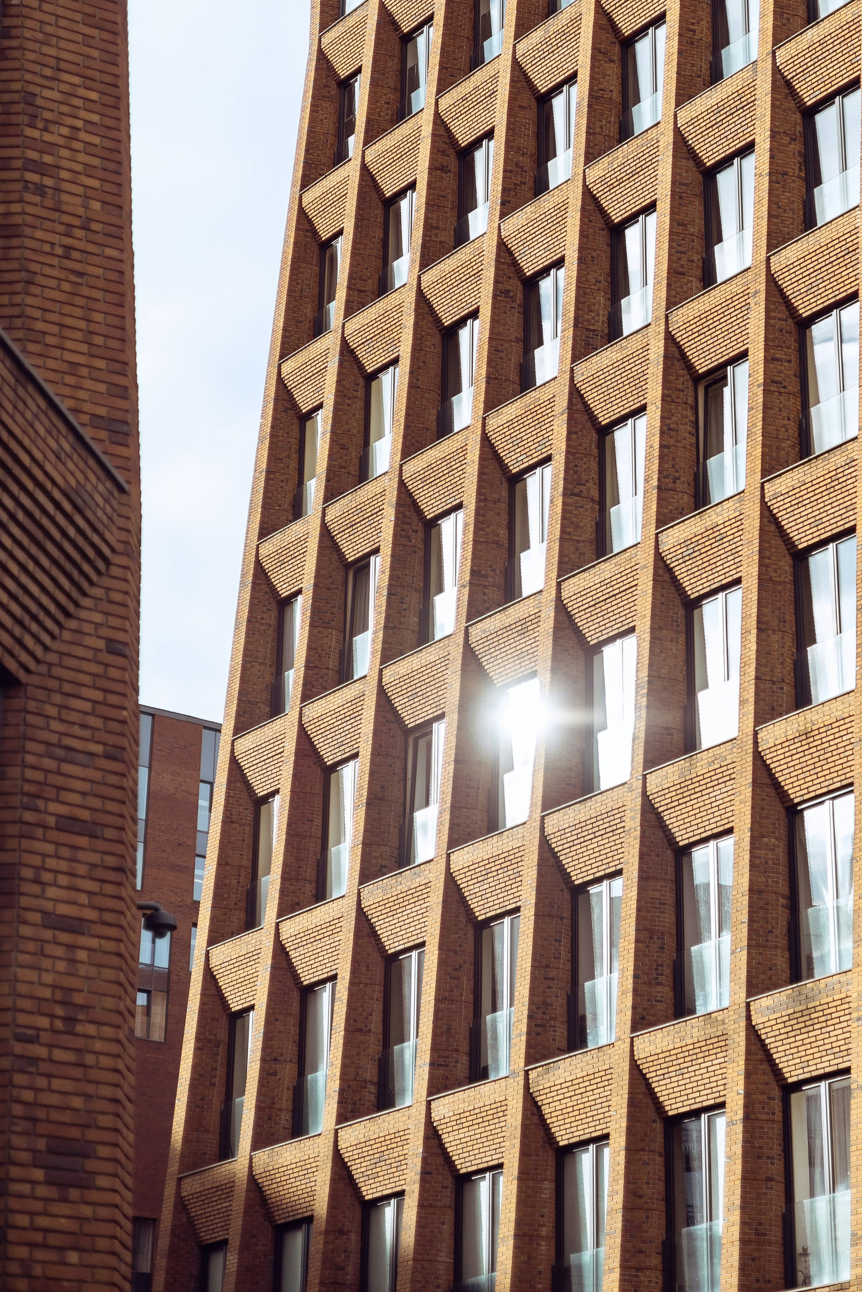 Brick-clad office building with repeating window patterns; sunlight reflects off a central pane, creating a bright flare against a clear sky.