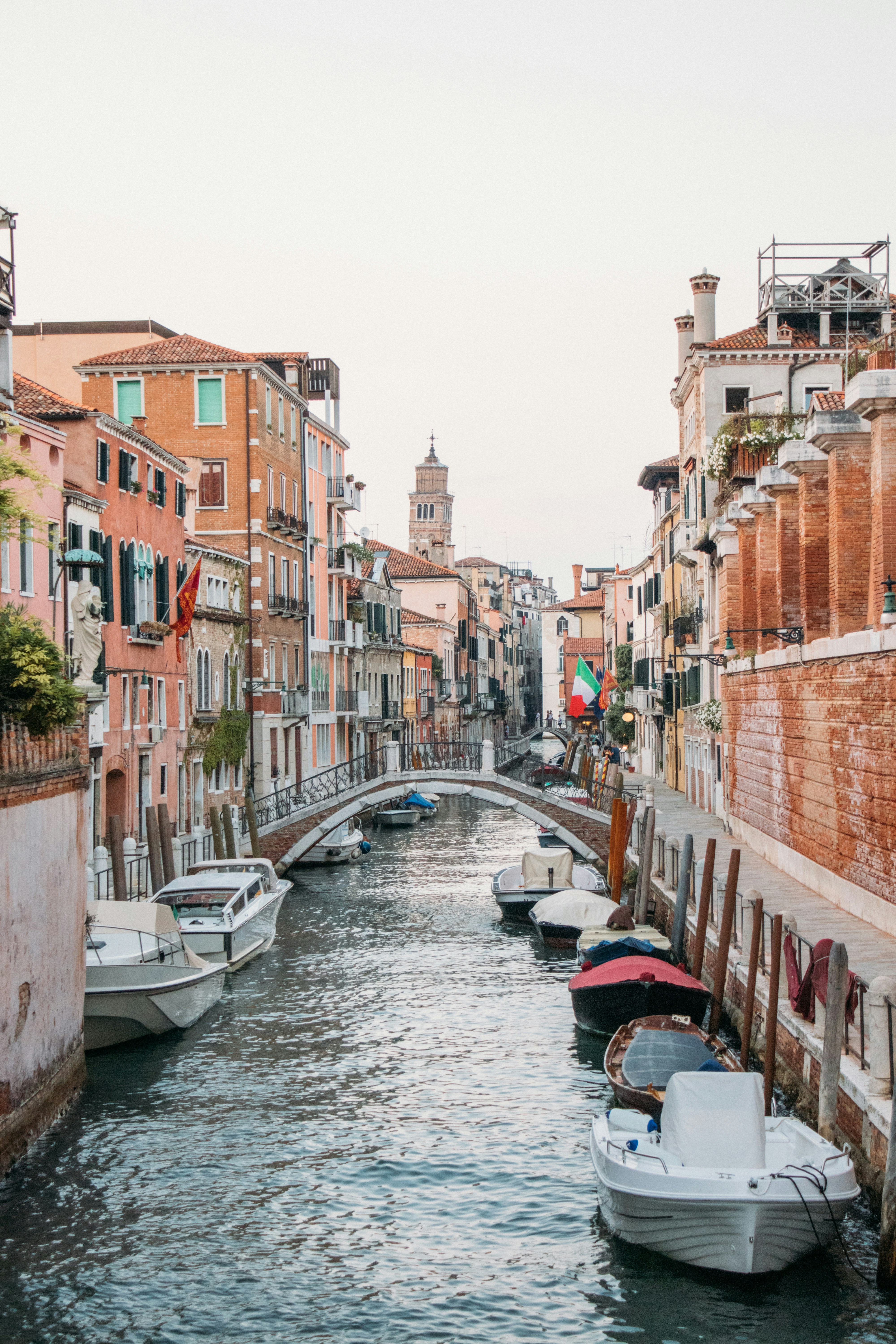 Venetian canal with boats, historic buildings, bridge, and bell tower.