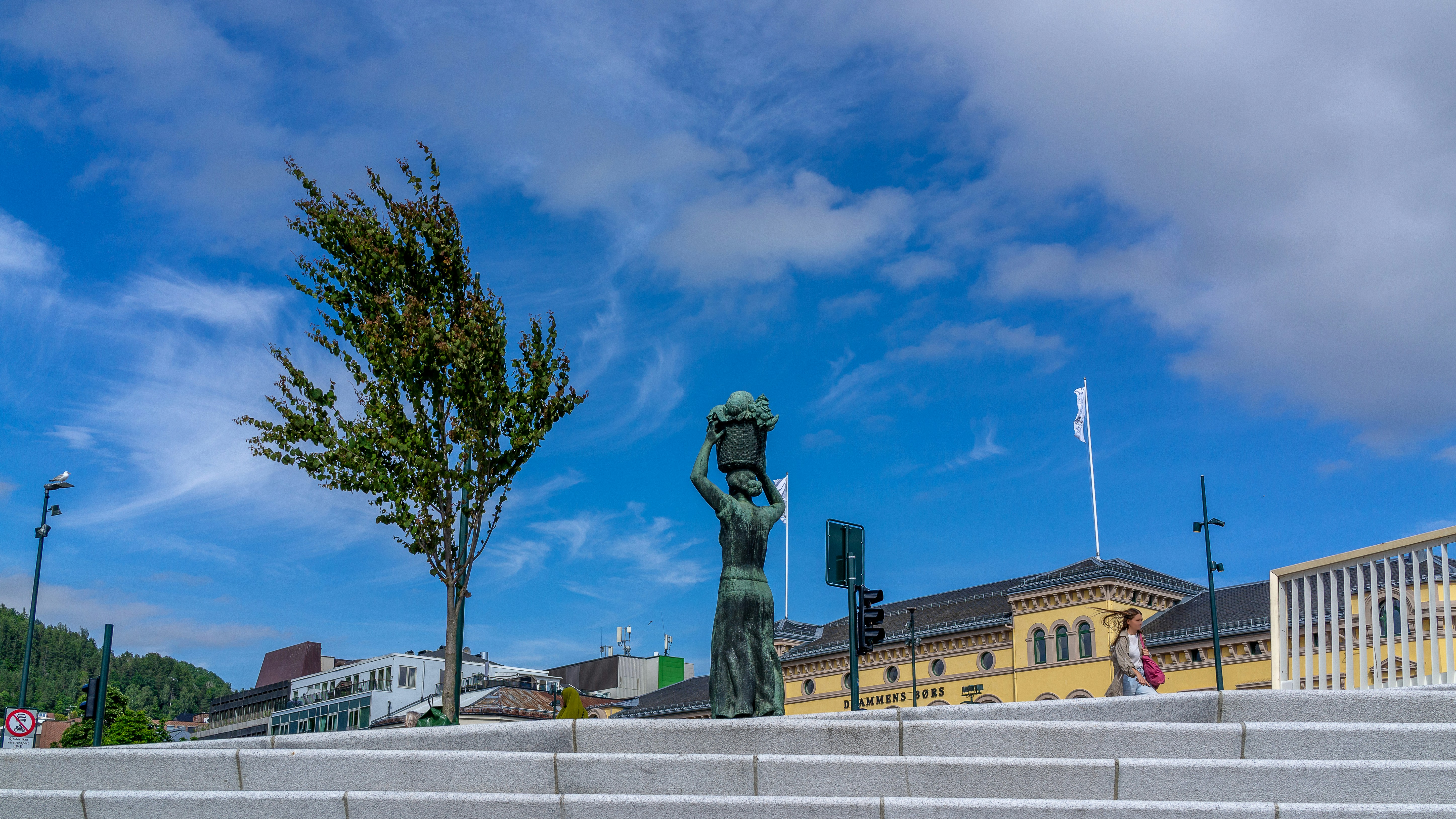 Bronze statue on a sunlit plaza under a windy sky