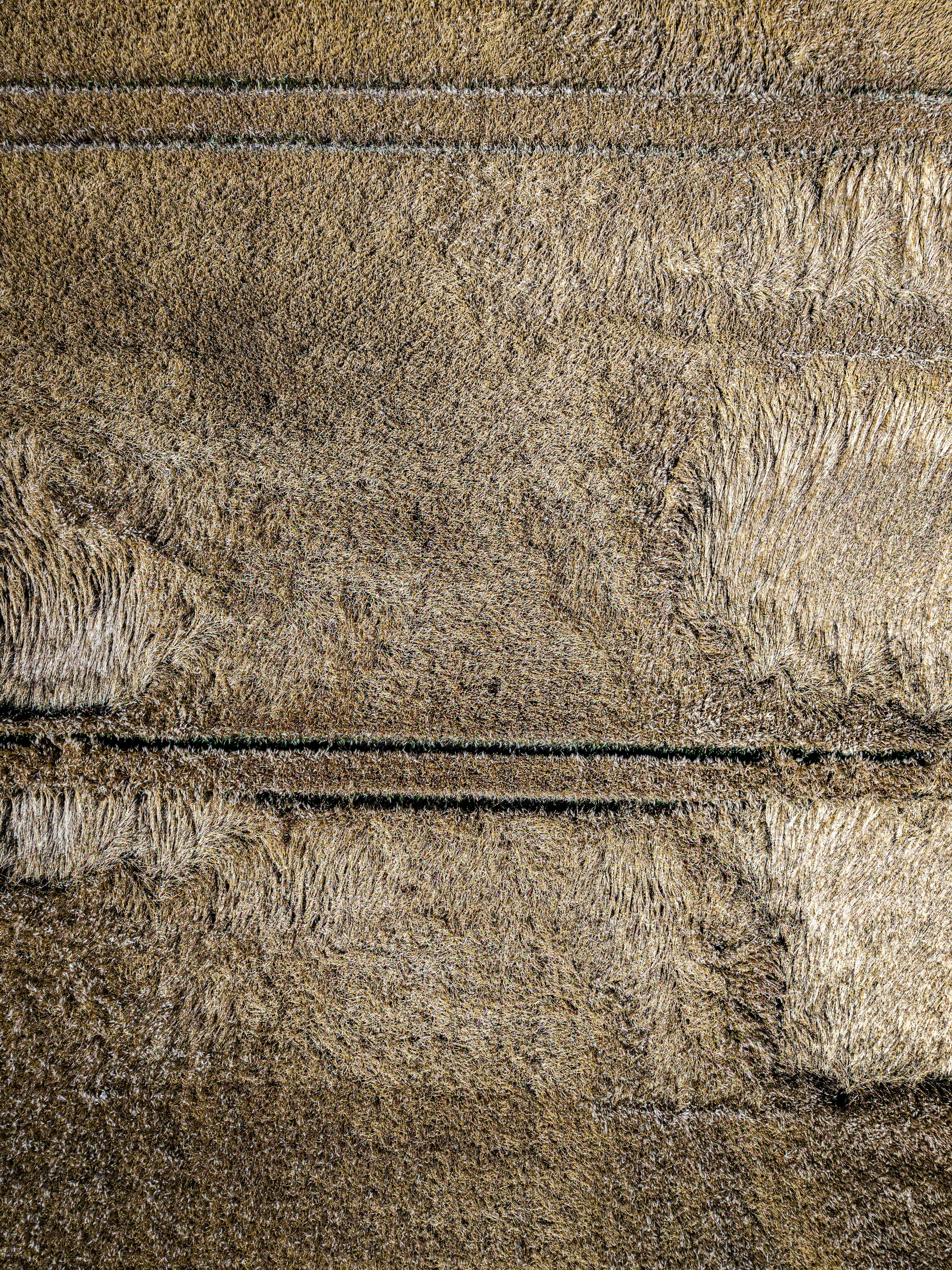 Close-up of textured sand with linear ridges and subtle shadow lines, emphasizing tactile surface patterns and natural gradients.