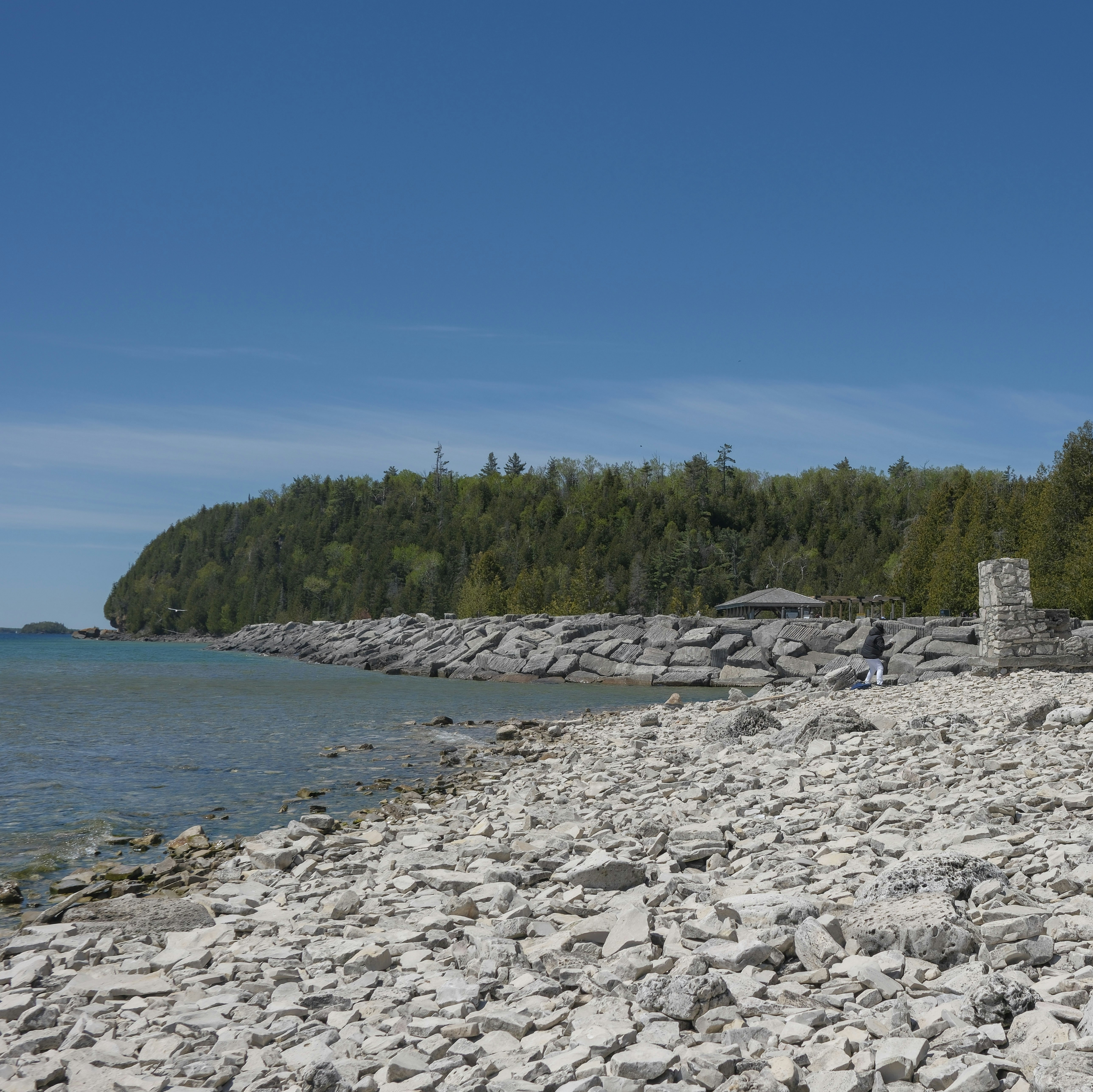 Rocky shoreline under blue sky with forested headland