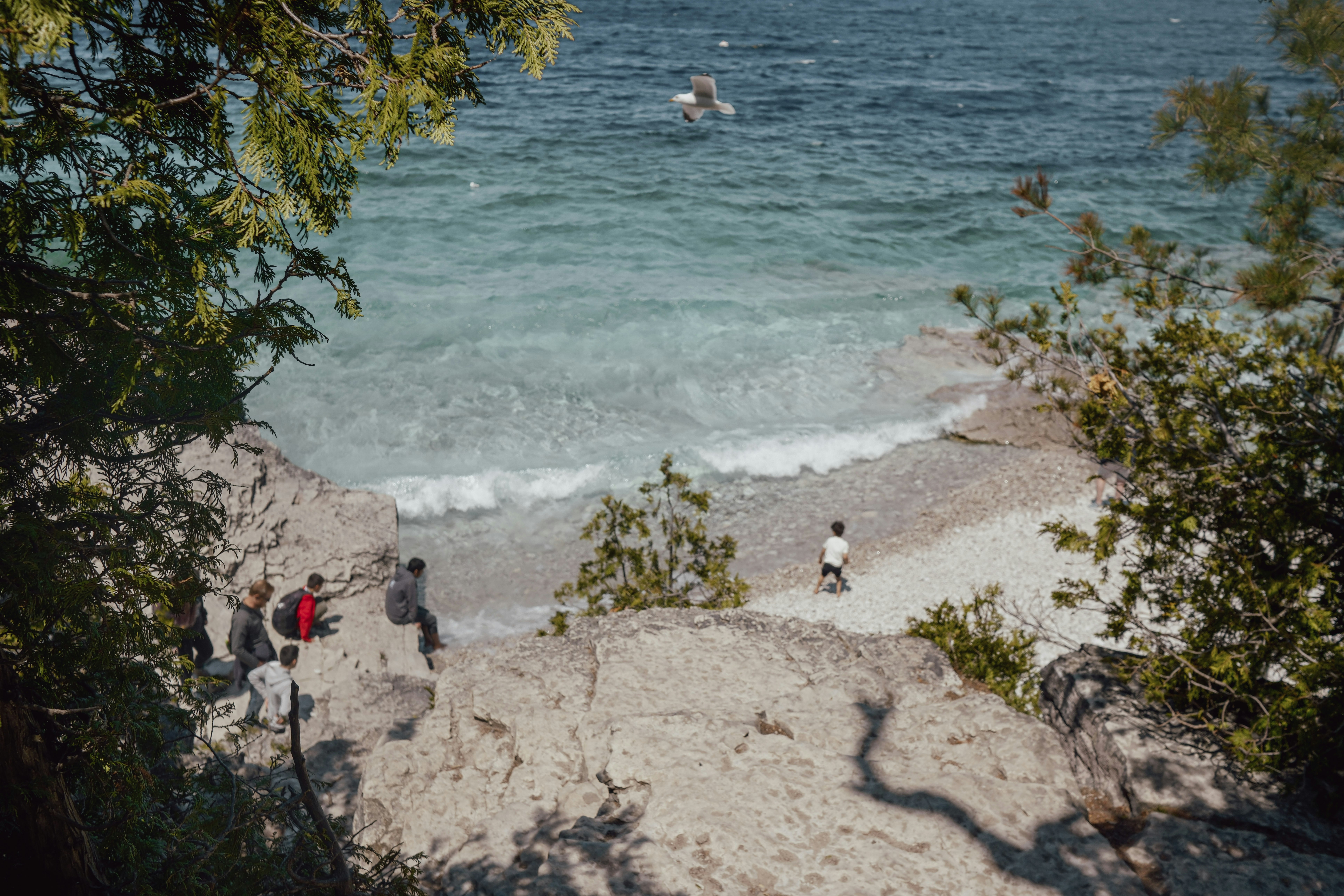 Cliffside Cove: People exploring a turquoise sea cove from above