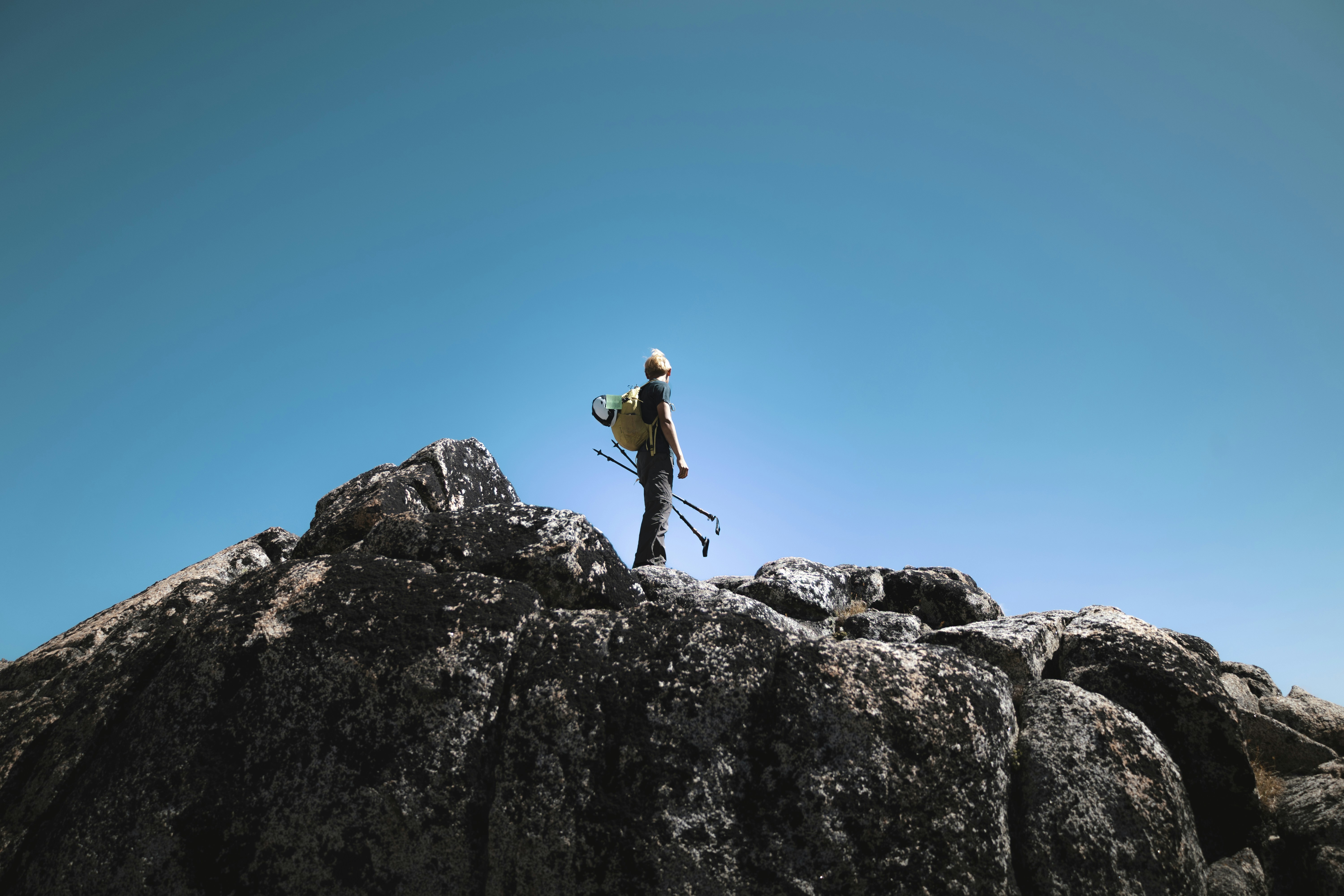 A lone climber stands atop rugged granite against a clear blue sky, conveying solitude and ascent.