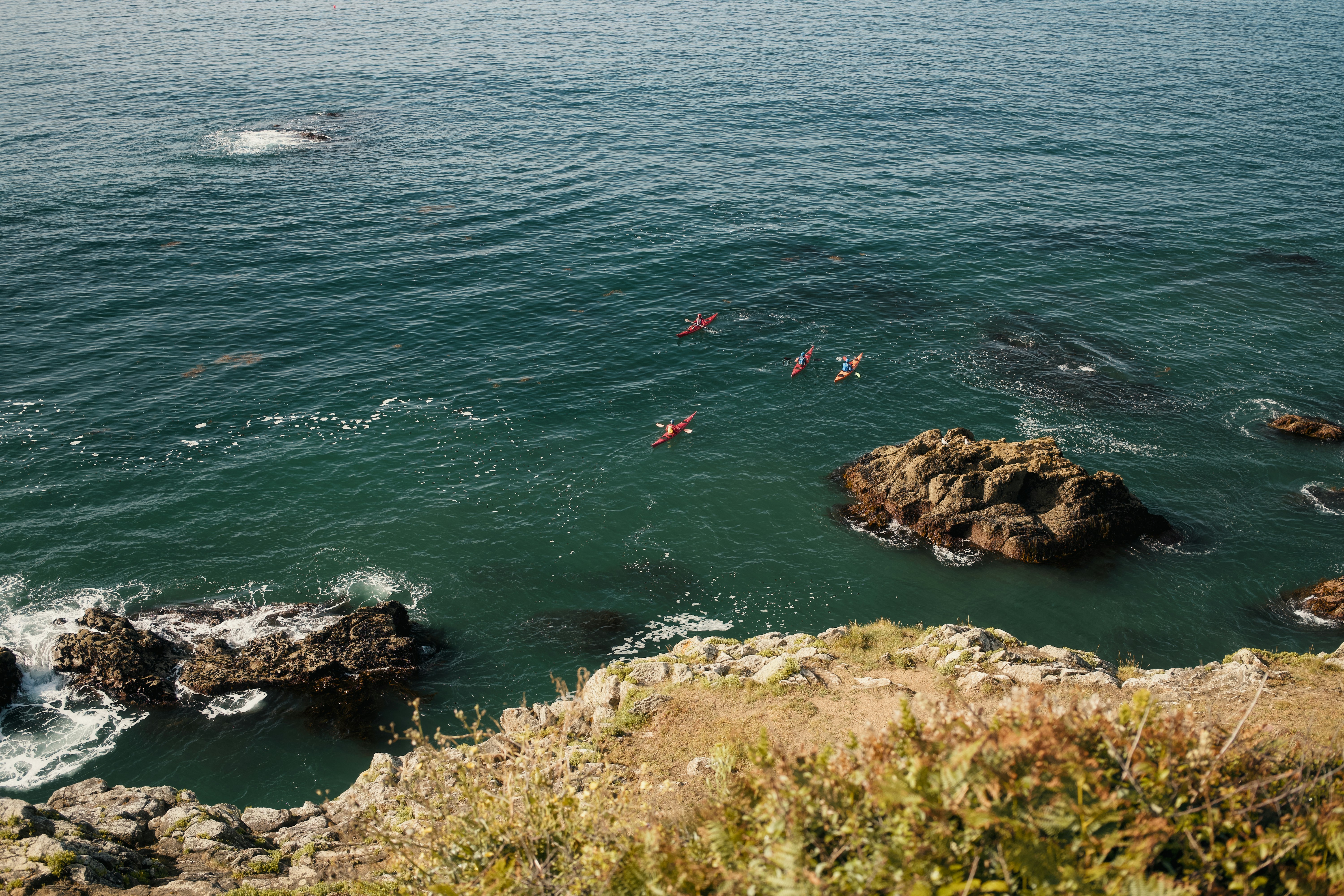 Red-sailed Rescue: Kayaks Near the Rugged Cove