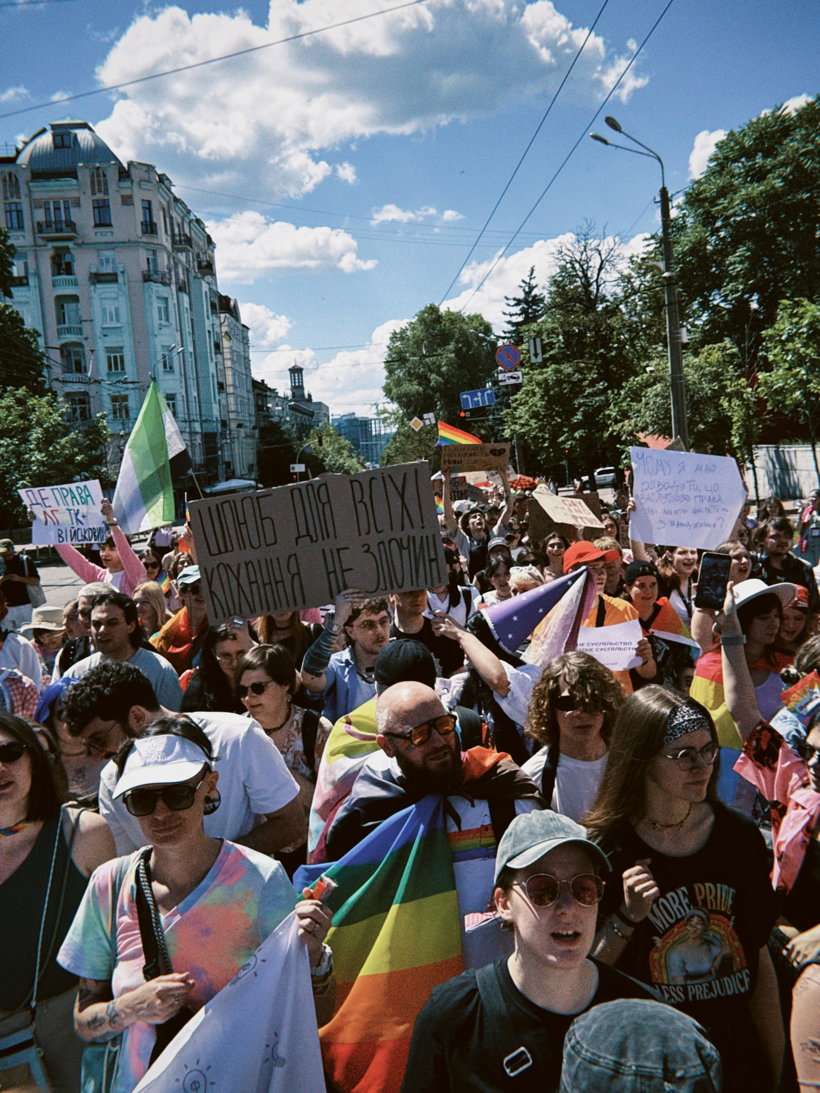 Crowd of Pride Flags and Signs marching through a sunlit city street