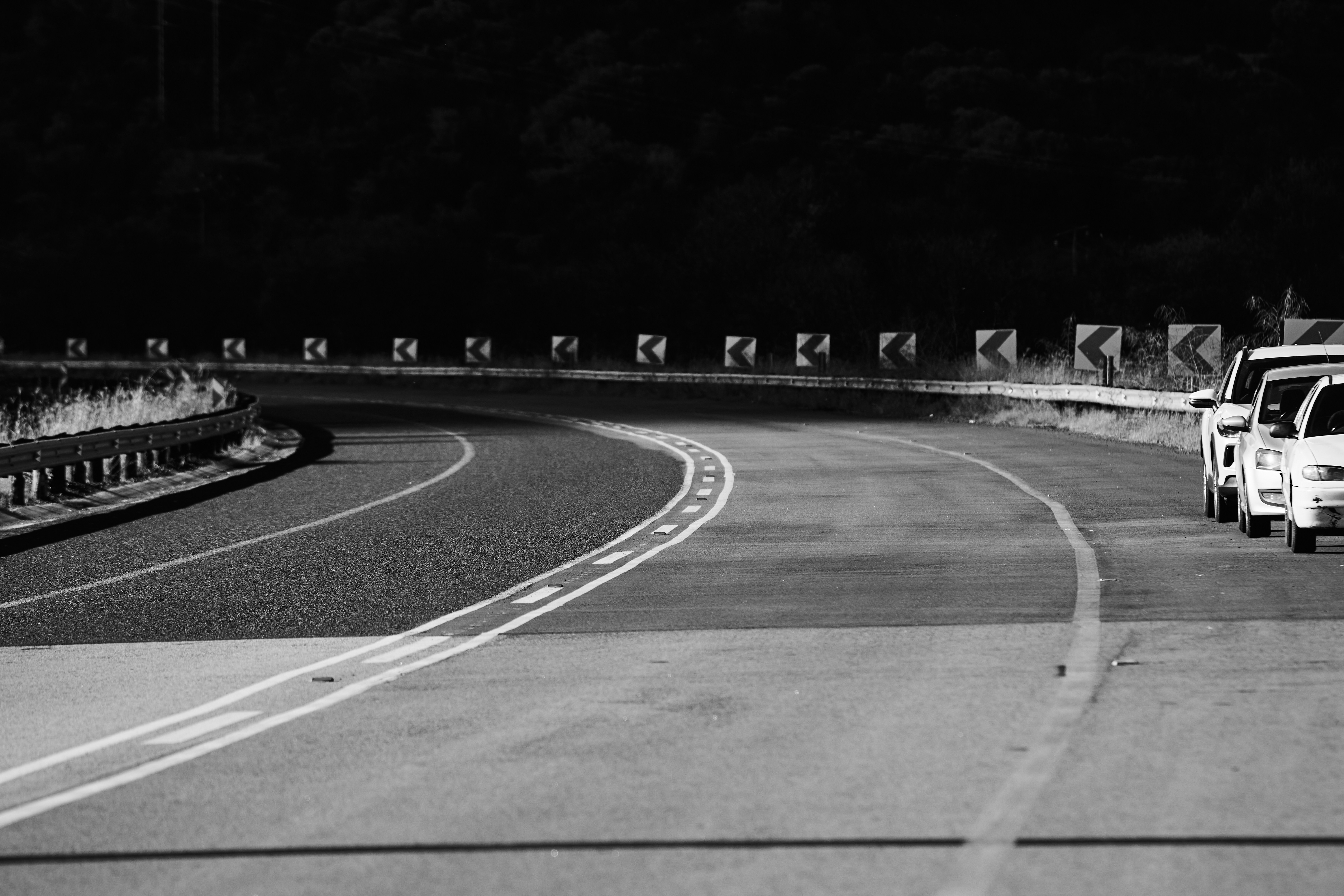 Roadside Mirage: A Black-and-White Curve of Cars at Dusk