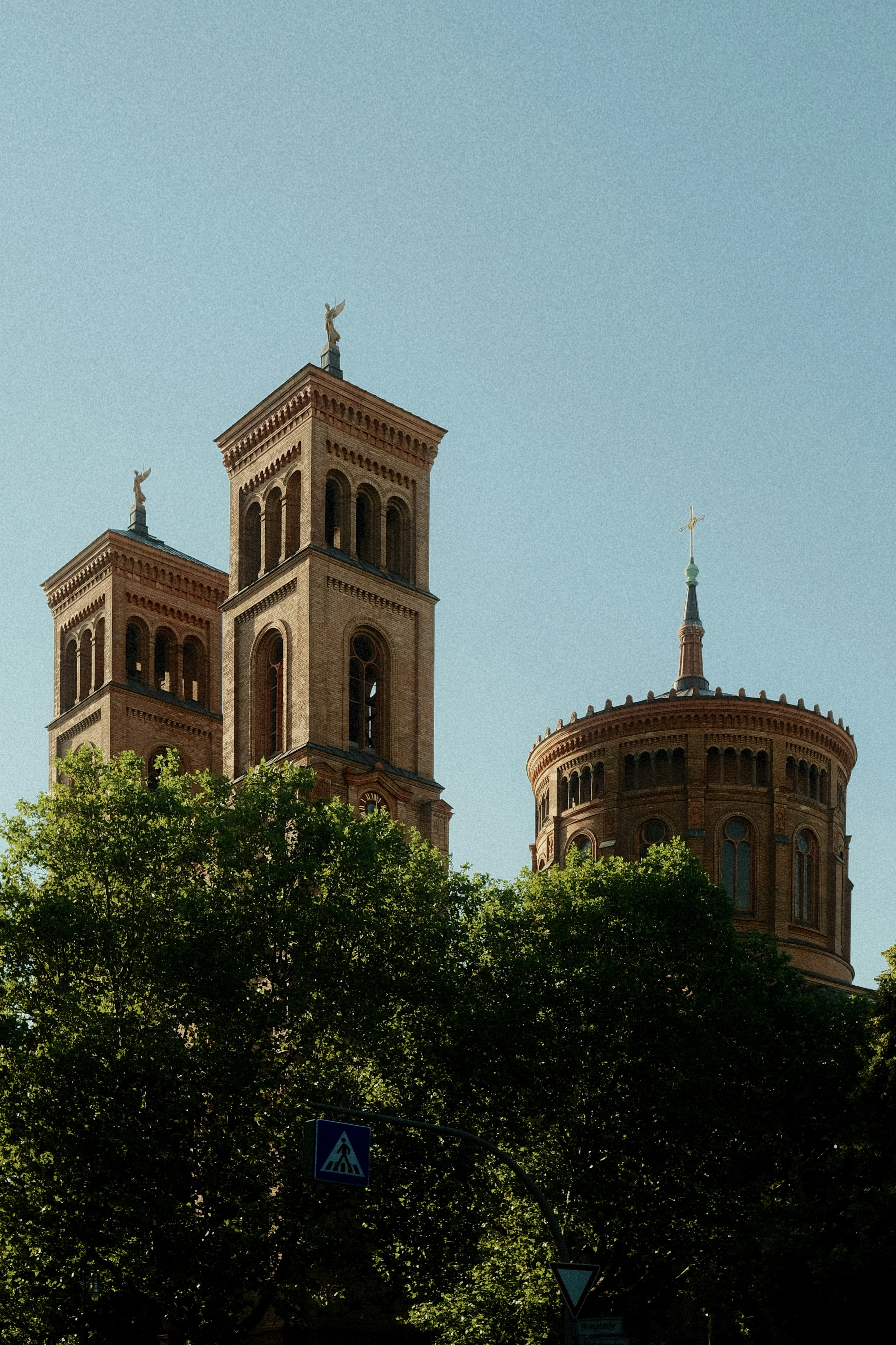 Brick bell-towers rising above emerald foliage under a crisp blue sky
