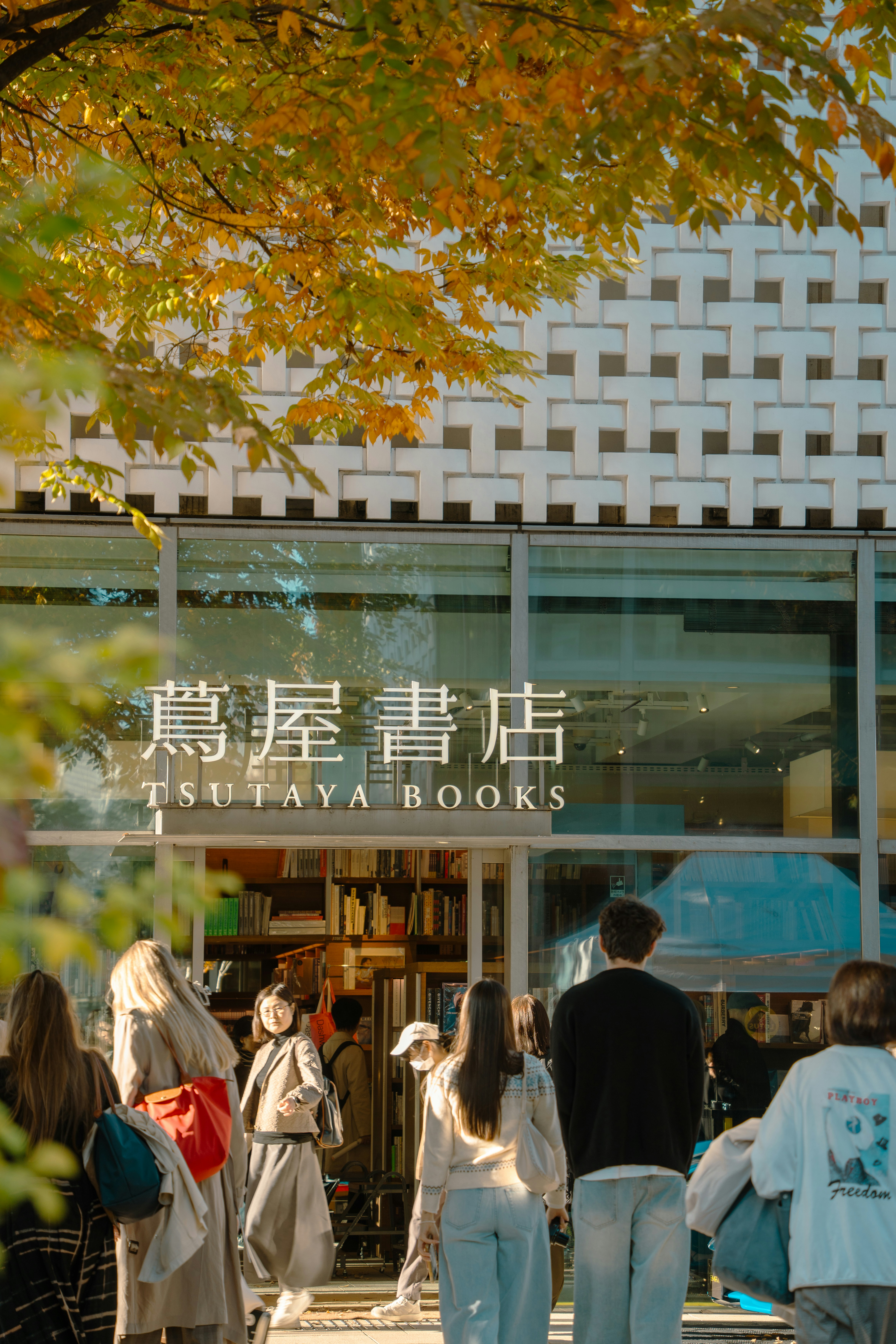 People gather at a bookstore storefront with bold signage in a sunlit urban scene