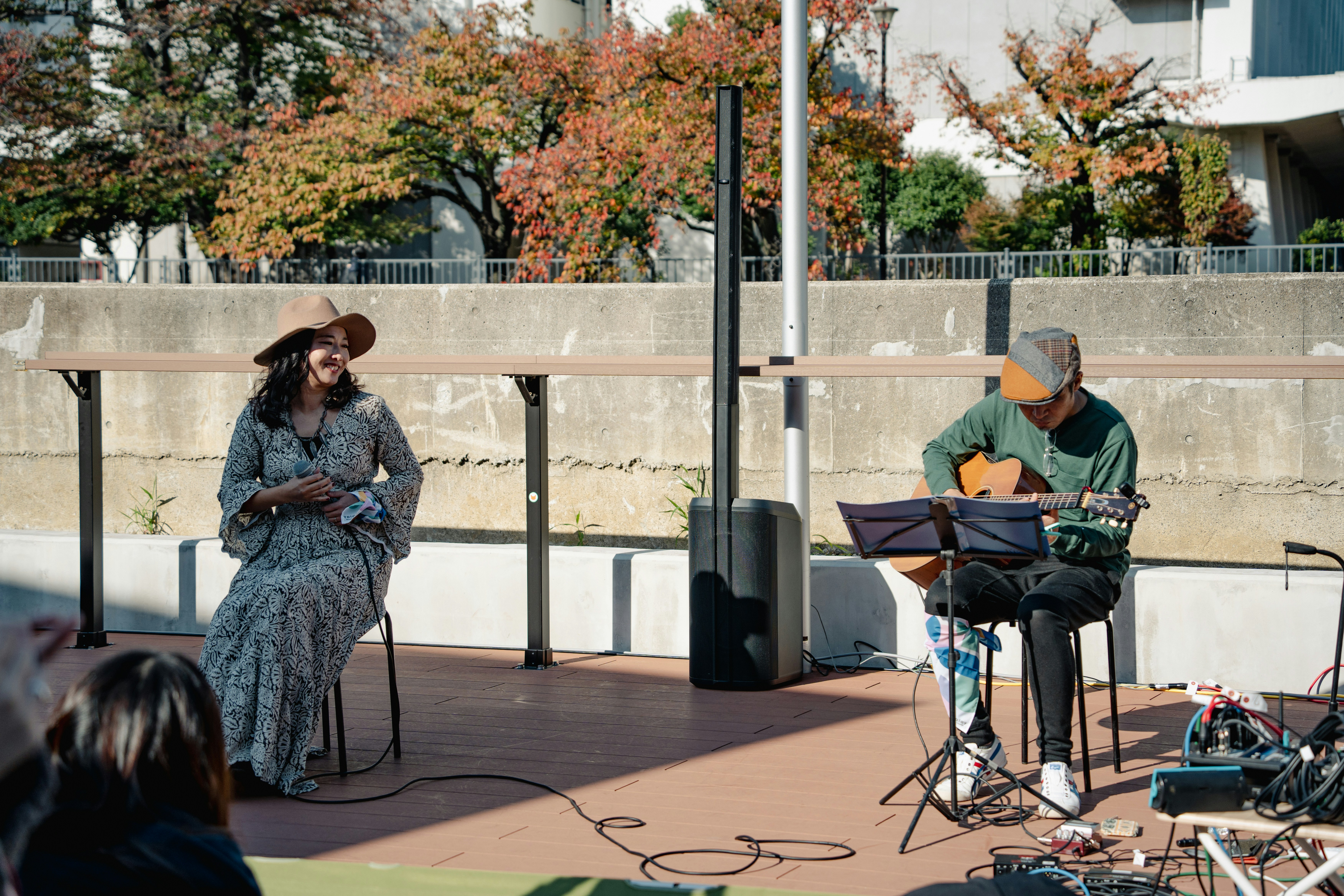 Duet on the Open Stage: A guitarist and a woman in a sunlit outdoor performance