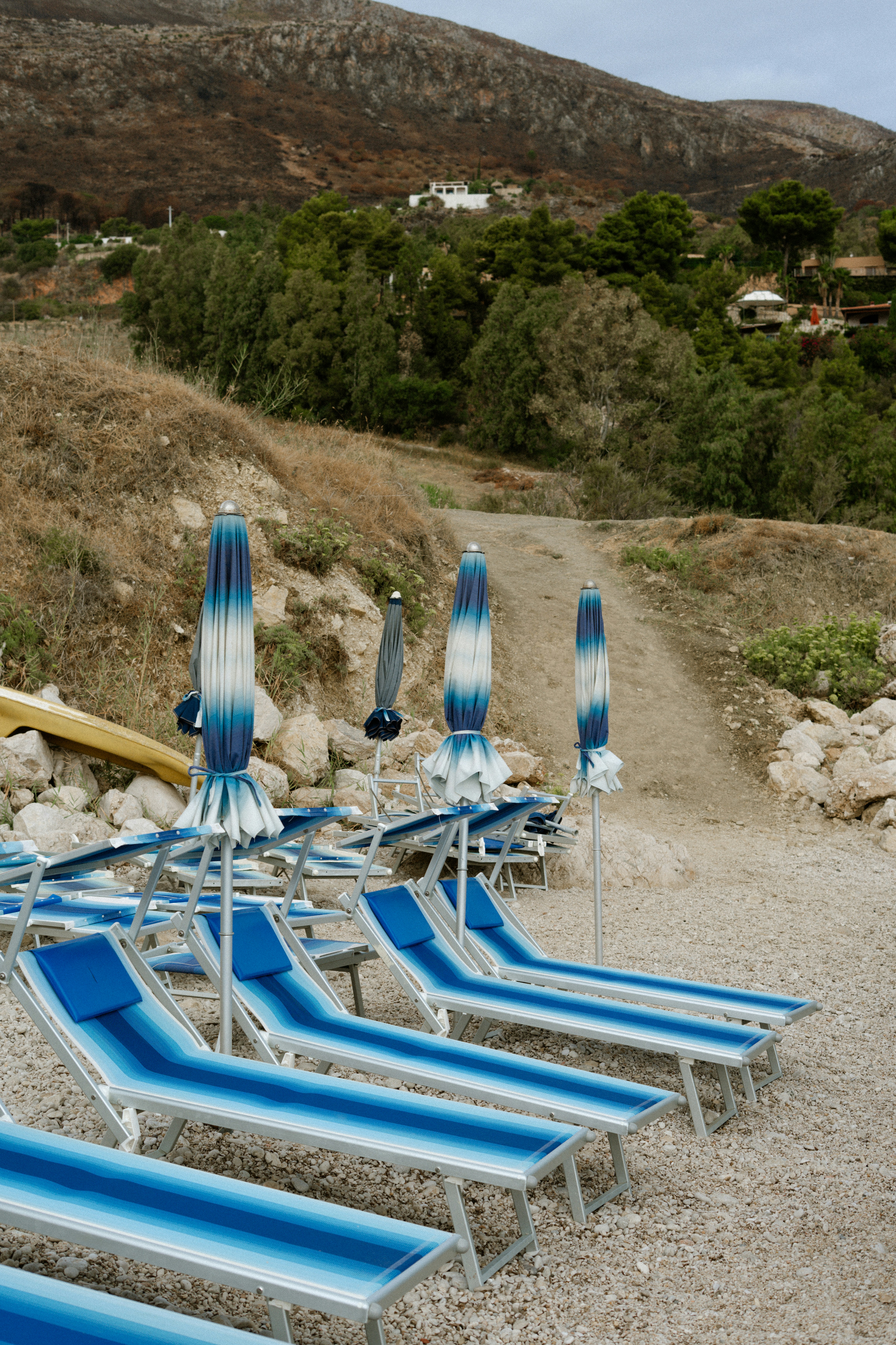 Row of Blue Striped Loungers Resting Before a Mountain Path