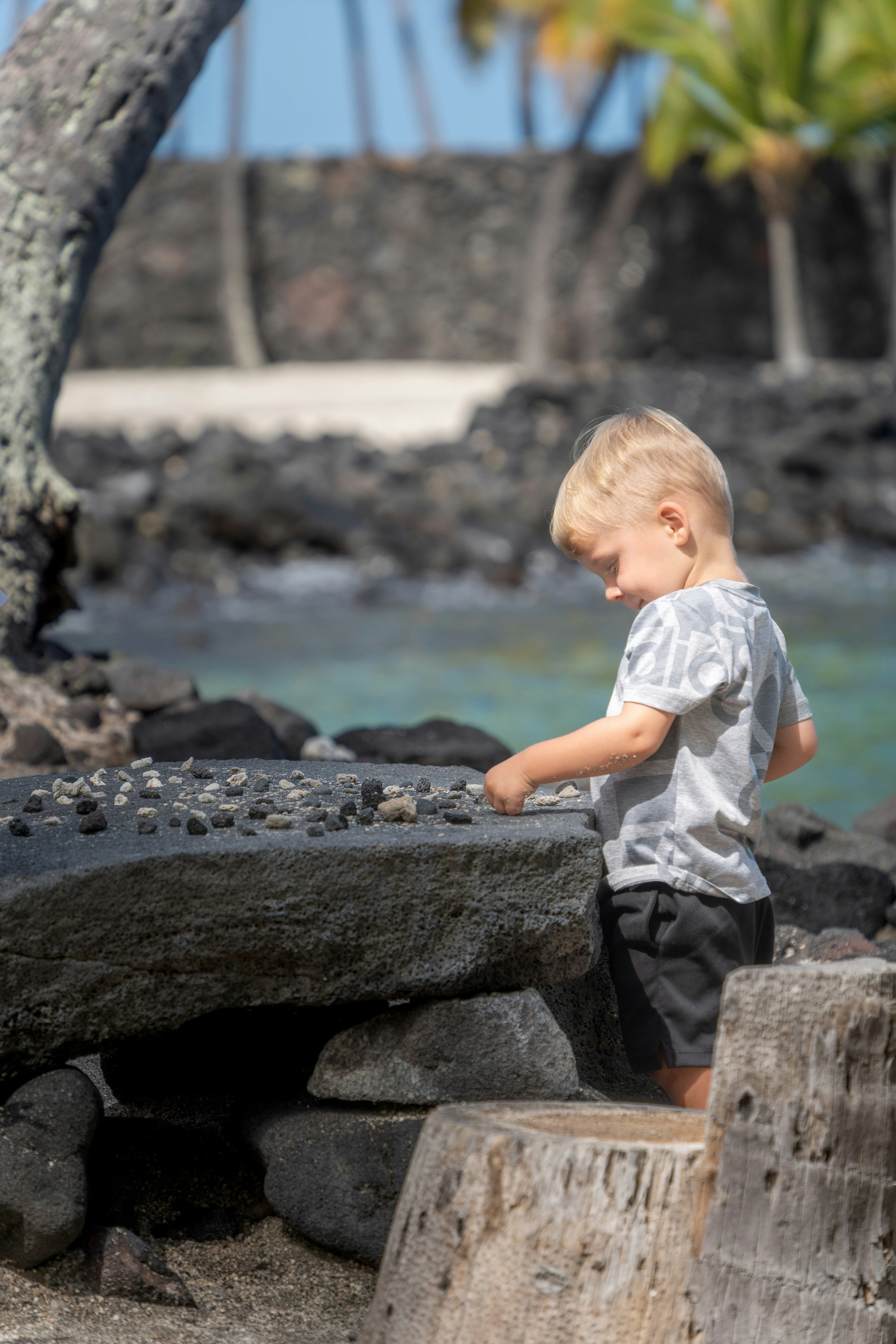 A young boy plays with stones on a rock structure.
