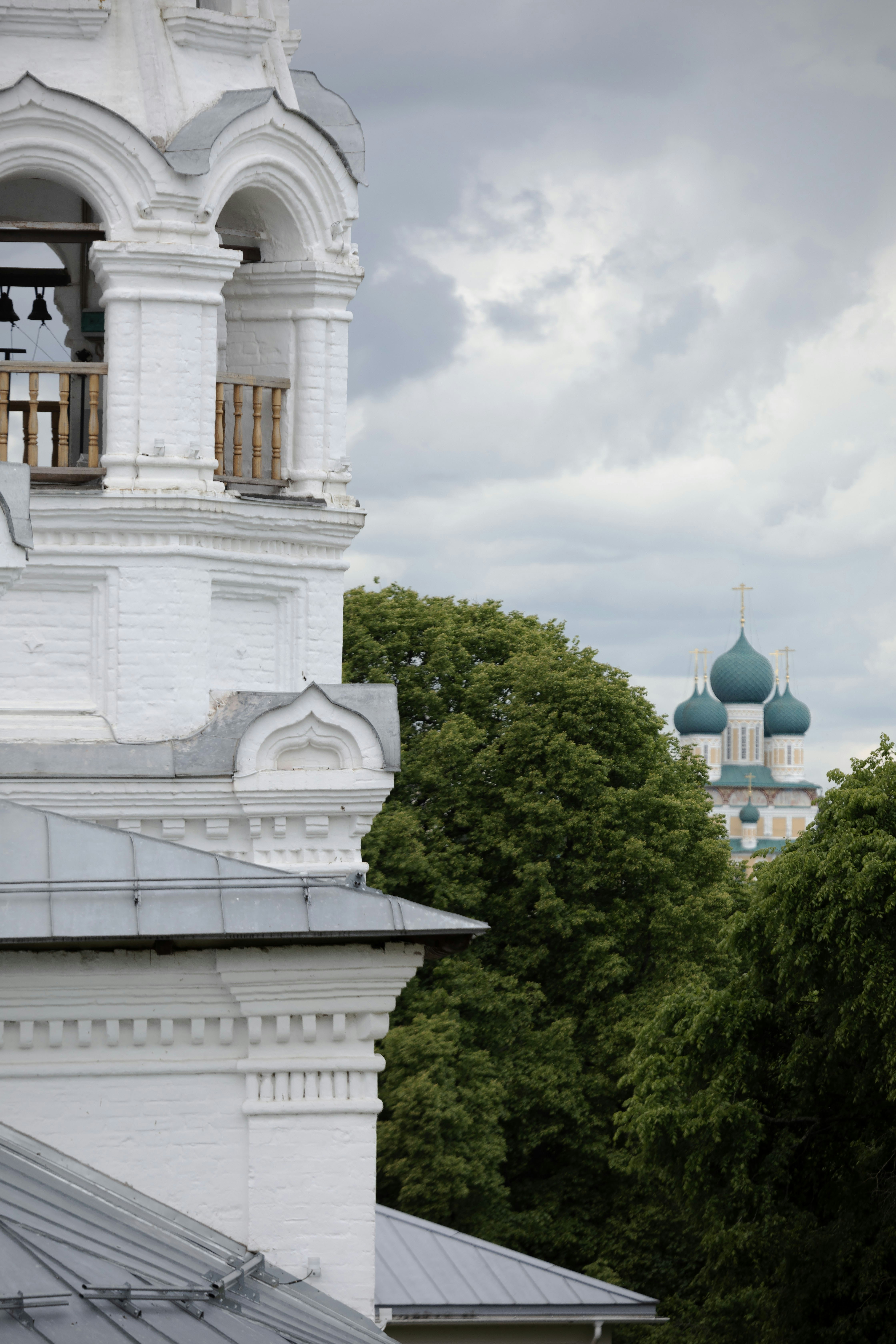 White Bell Tower and Emerald Domes: A Cathedral Peering Through Green Canopy