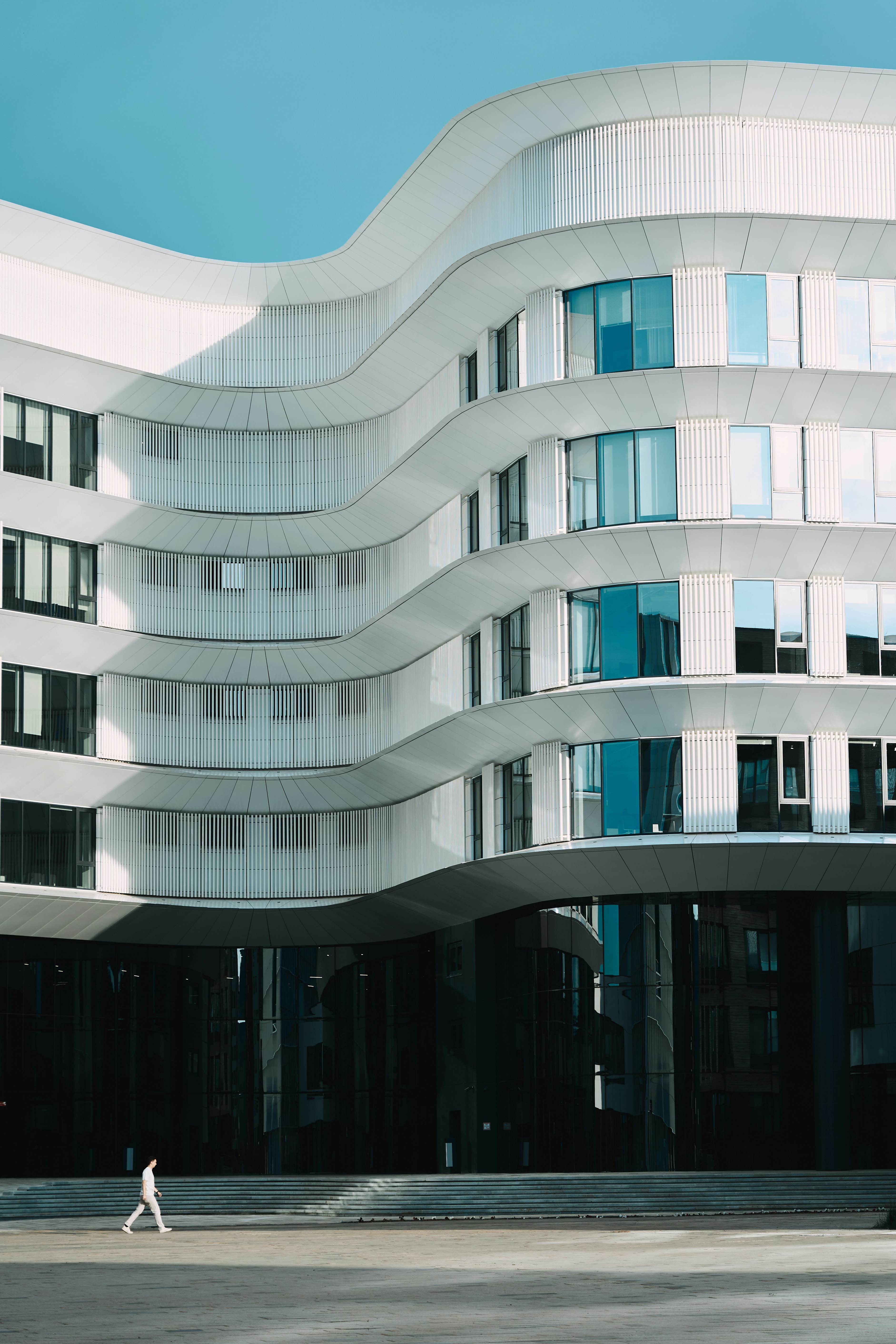 Flowing White Waves: A Modern Facade with a Lone Pedestrian
