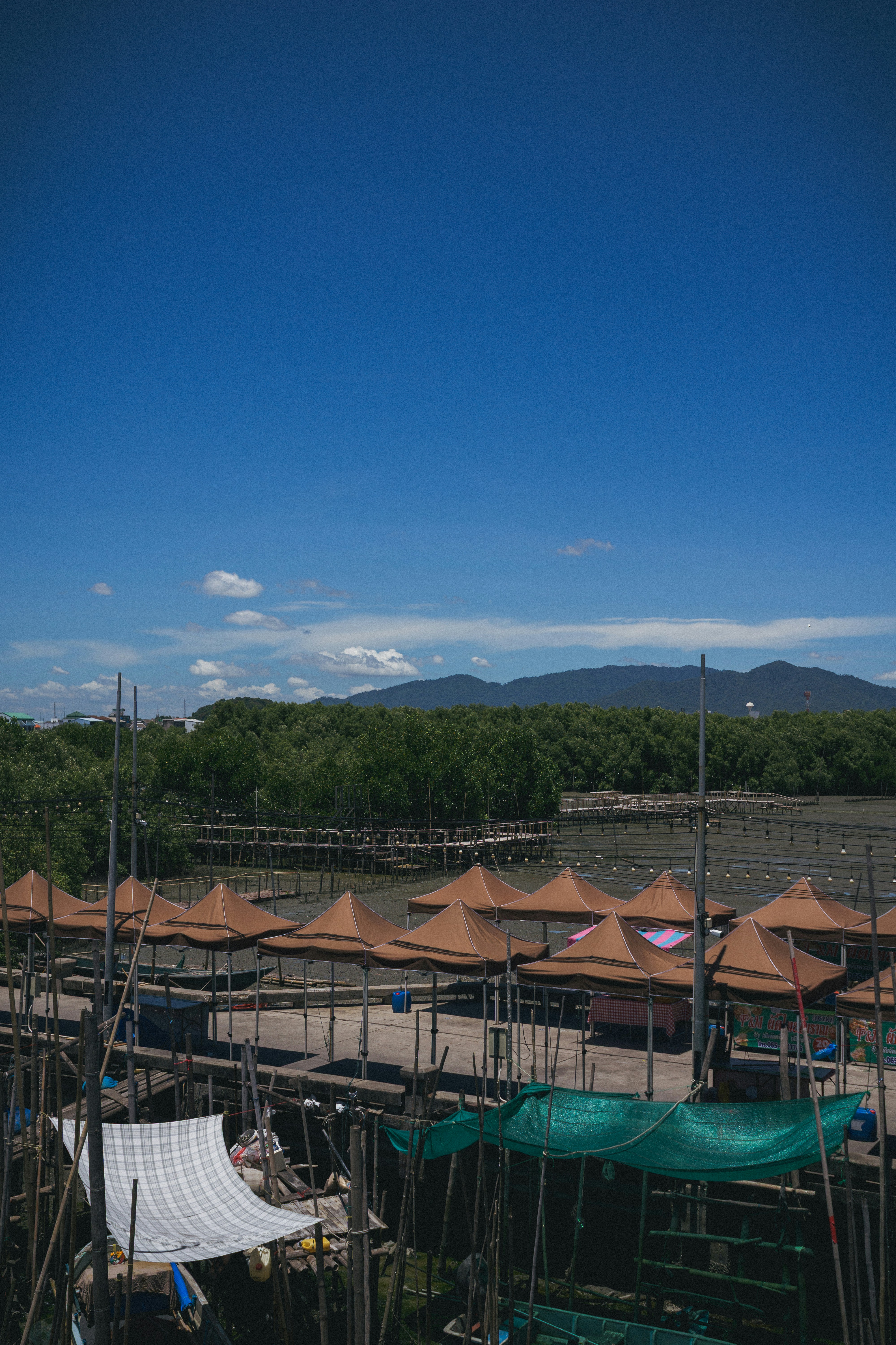 Row of shaded tents over a timber walkway by a calm water body