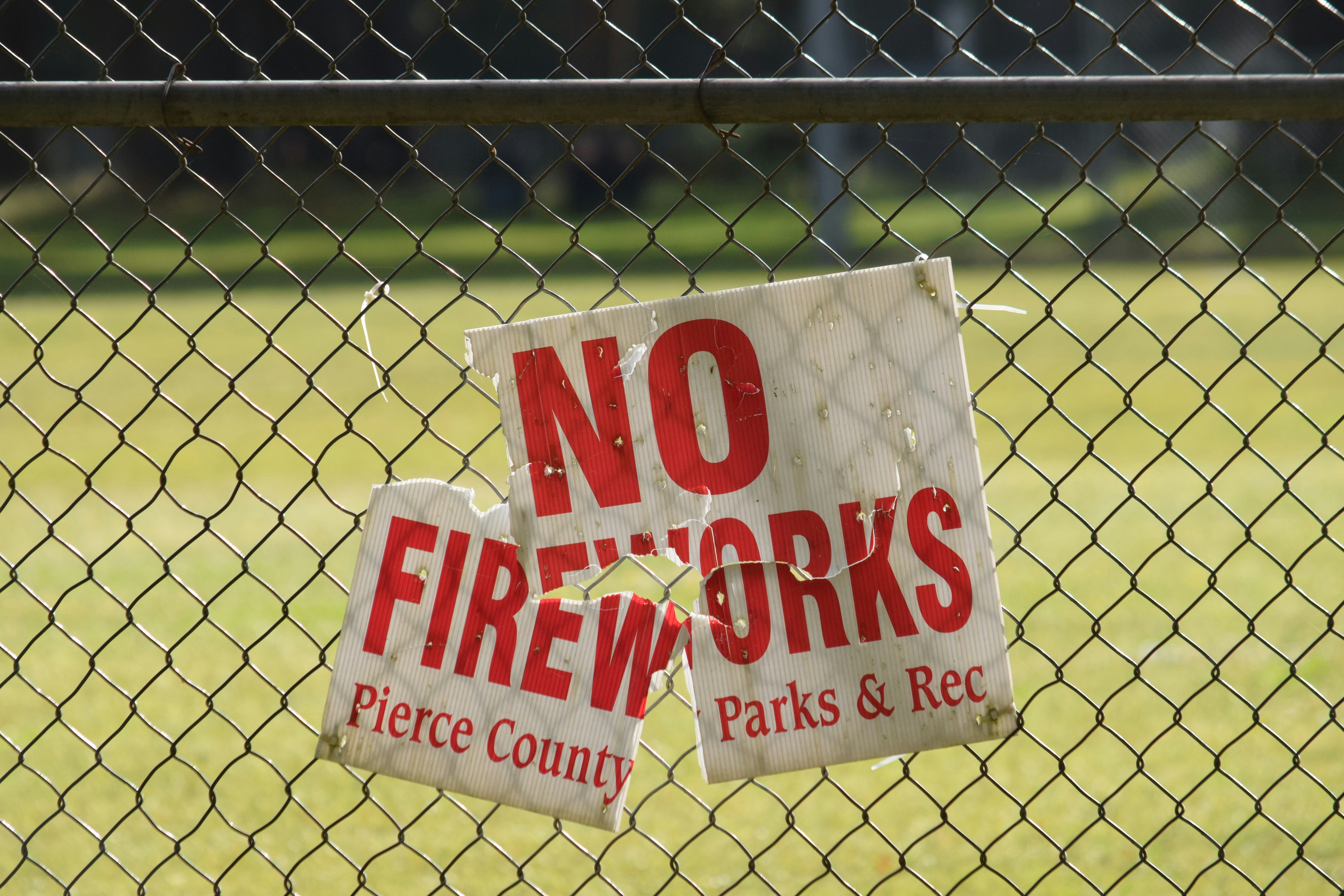 No Fireworks to Protect the Field: Weathered No-Fireworks Sign on Chain-Link Fence