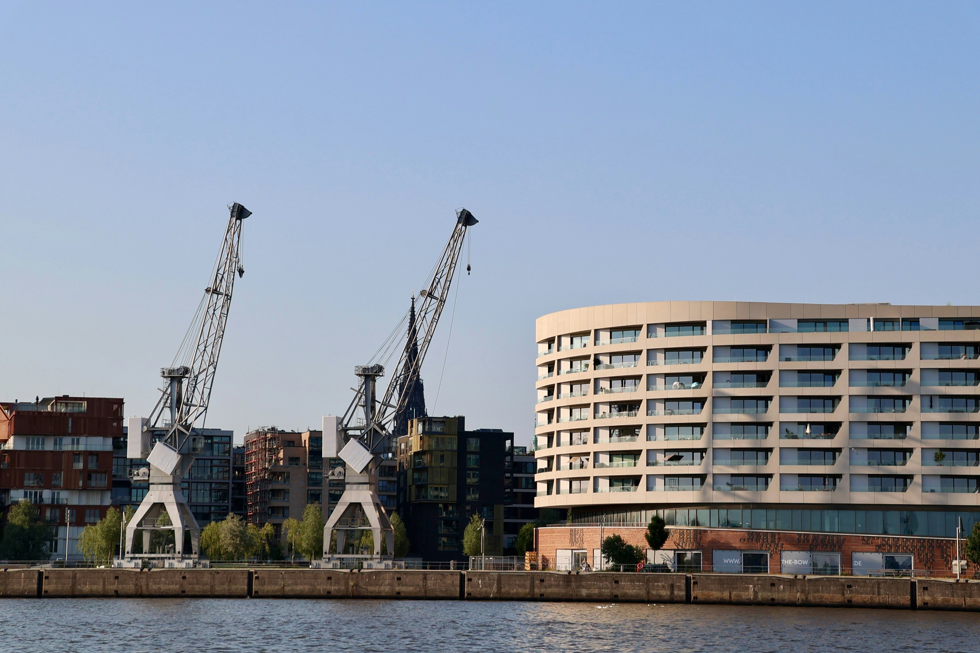 Crane silhouettes by a curved riverside office block