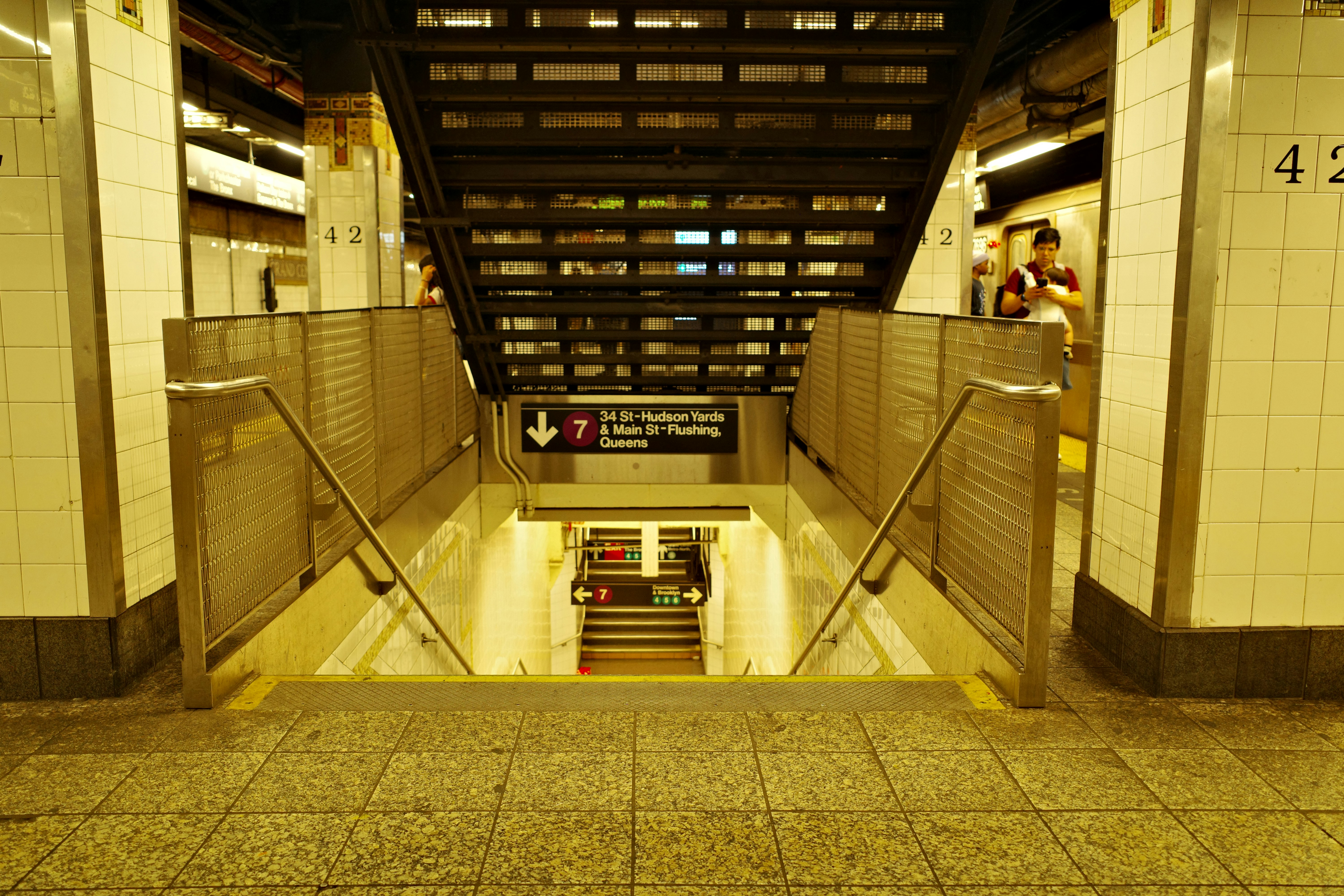 Subway stairwell leading down to platforms, with tiled walls and yellow safety edges. The scene captures an architectural moment of transition and movement within an underground station.
