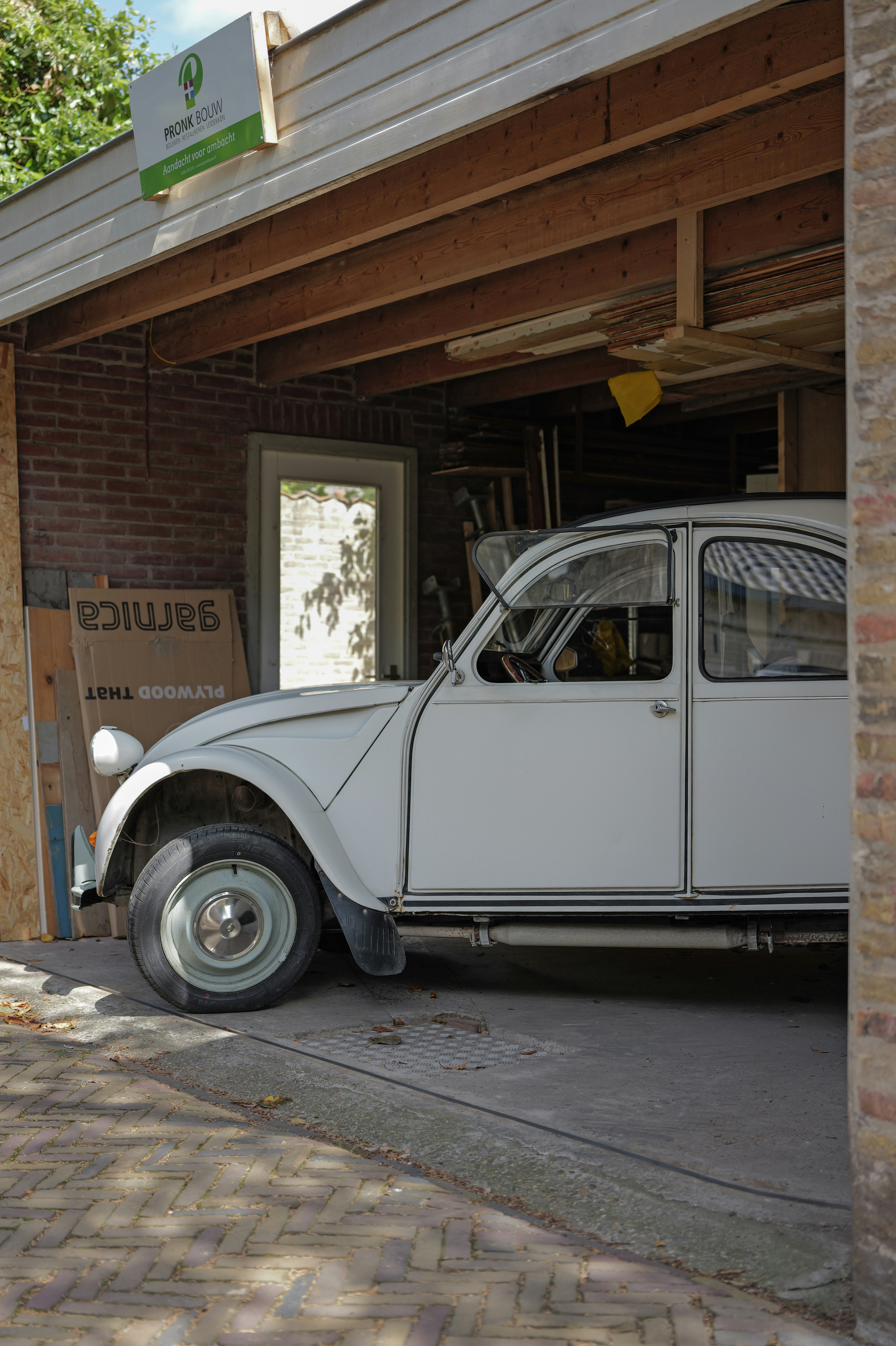 White vintage car parked inside a brick garage under a wooden beam