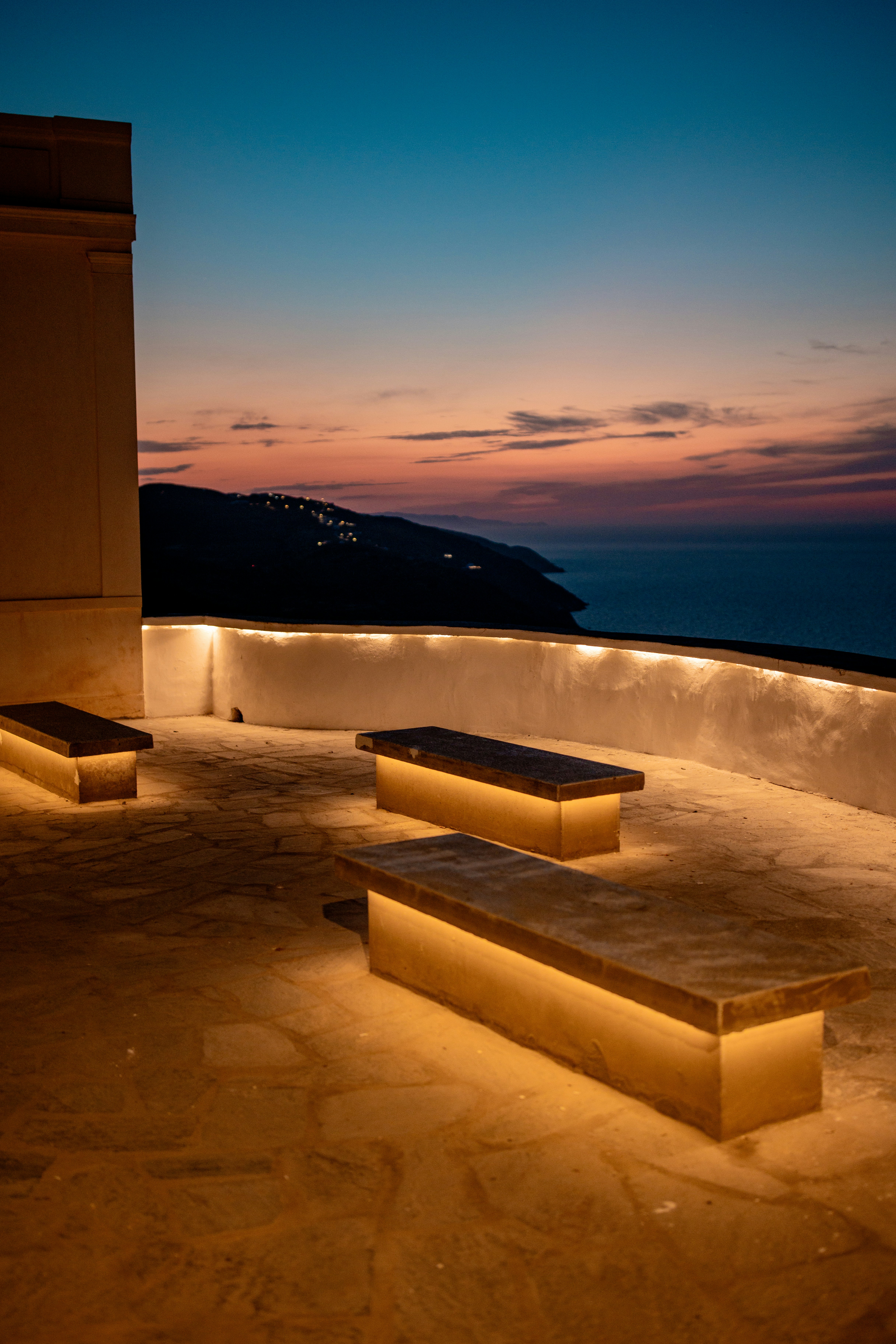 Terrace at Dusk: Warm Light Illuminates Stone Benches Against a Coastal Sunset