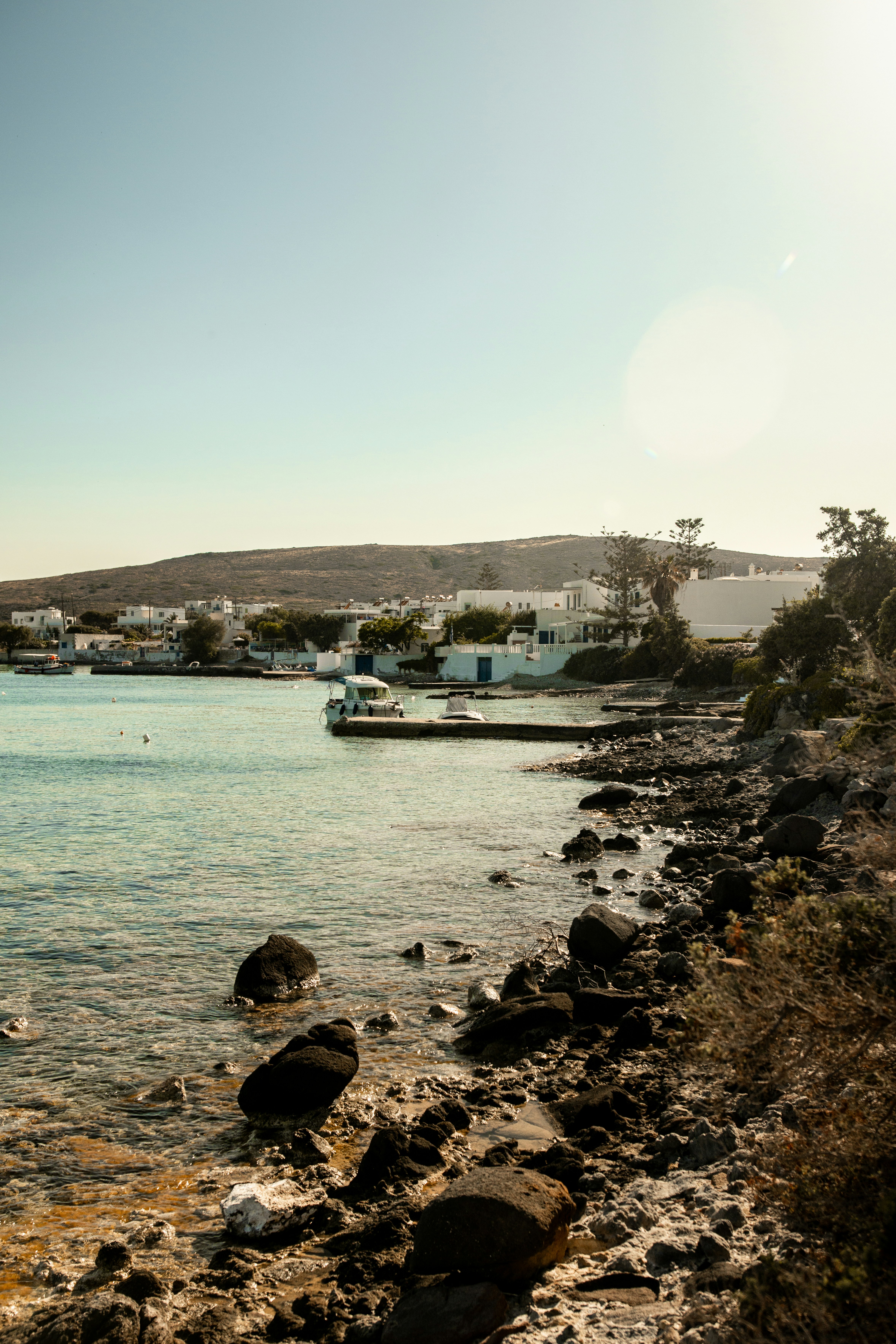 Sunlit shore of a quiet harbor with rocky coastline and distant town