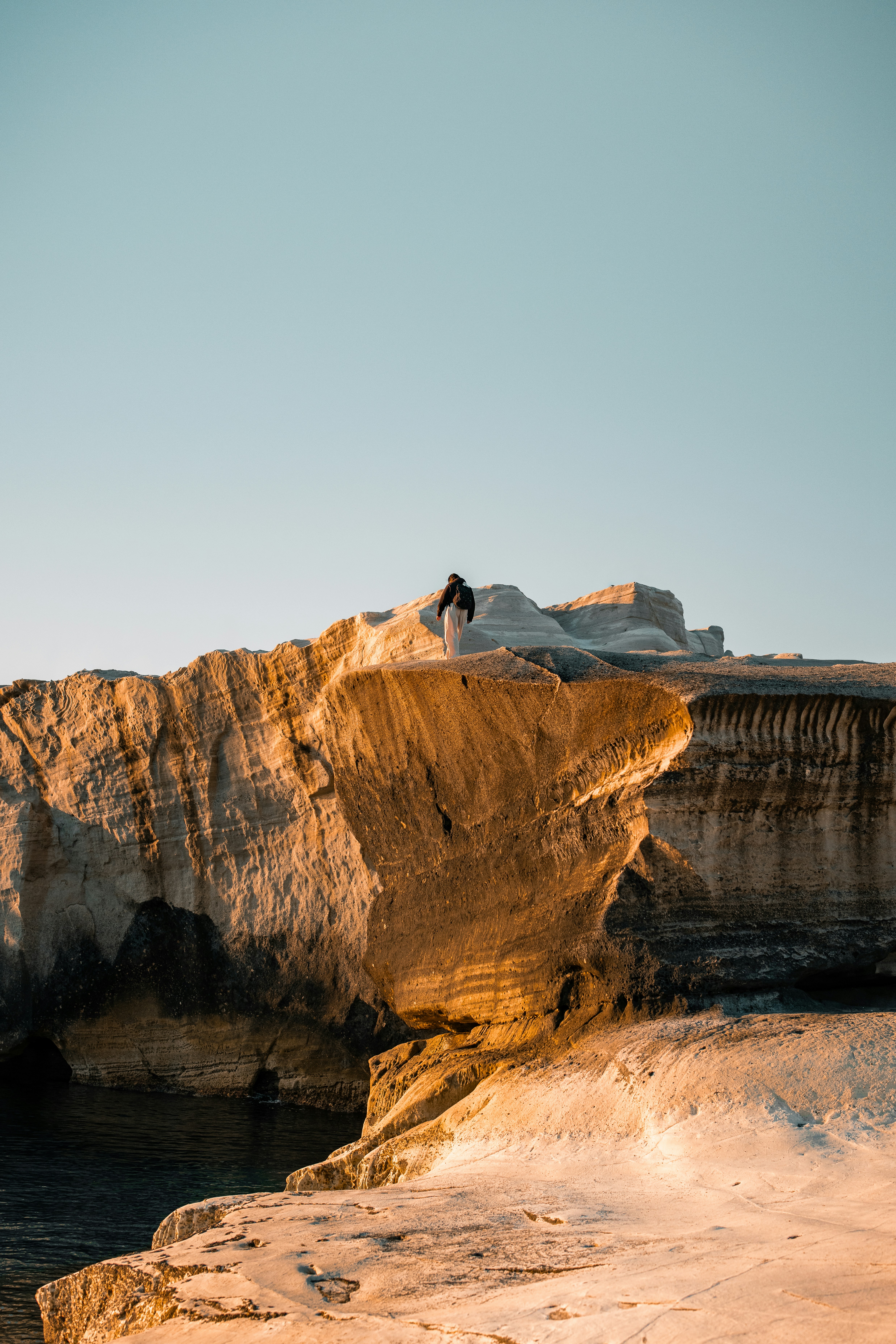 Sunlit Prominence: A Lone Figure on Carved Cliff Edge