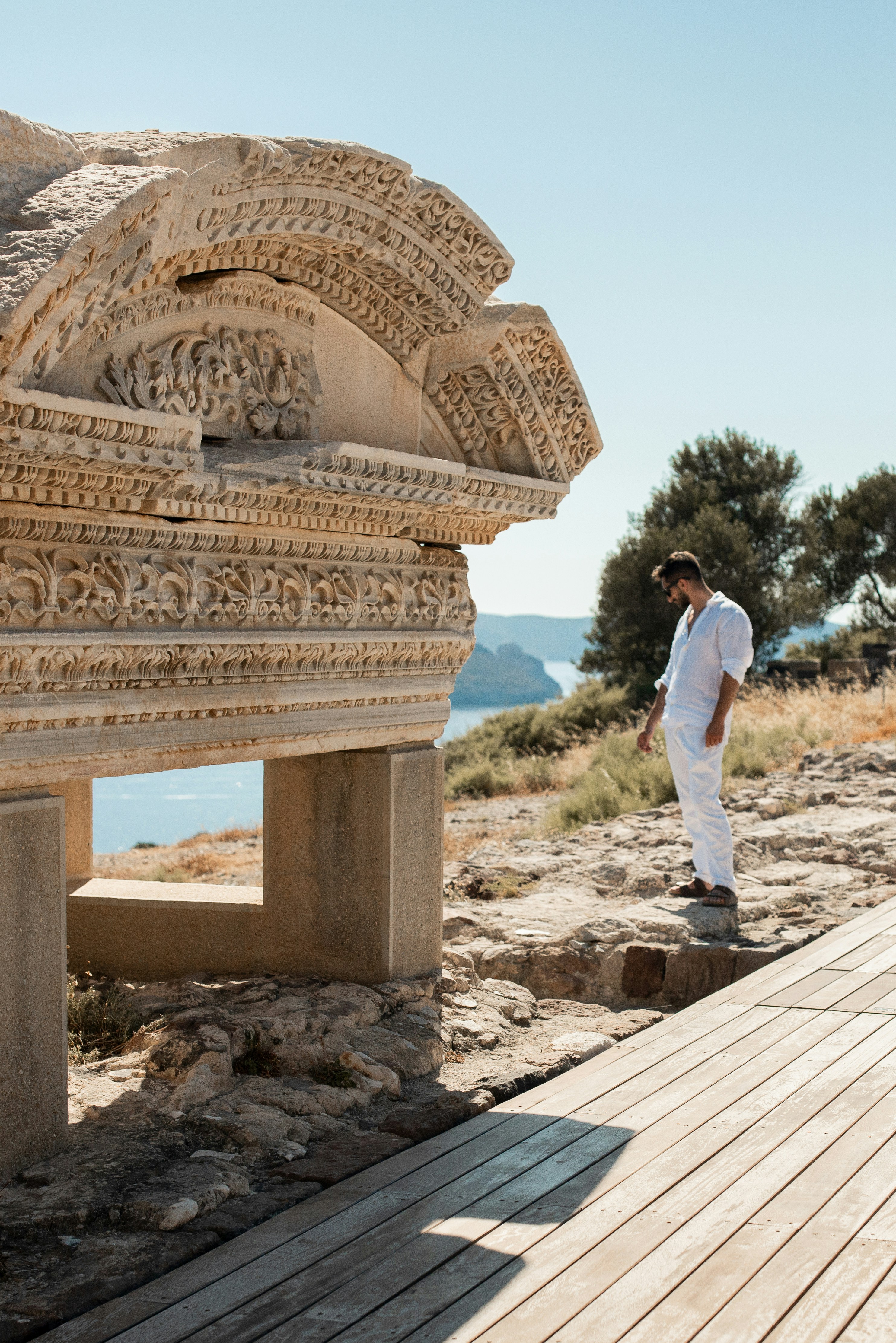 White-clad figure at an ancient carved frieze overlooking a coastal cliff